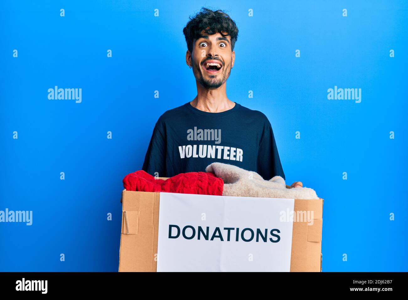 Young hispanic man holding donation box with clothes celebrating crazy ...
