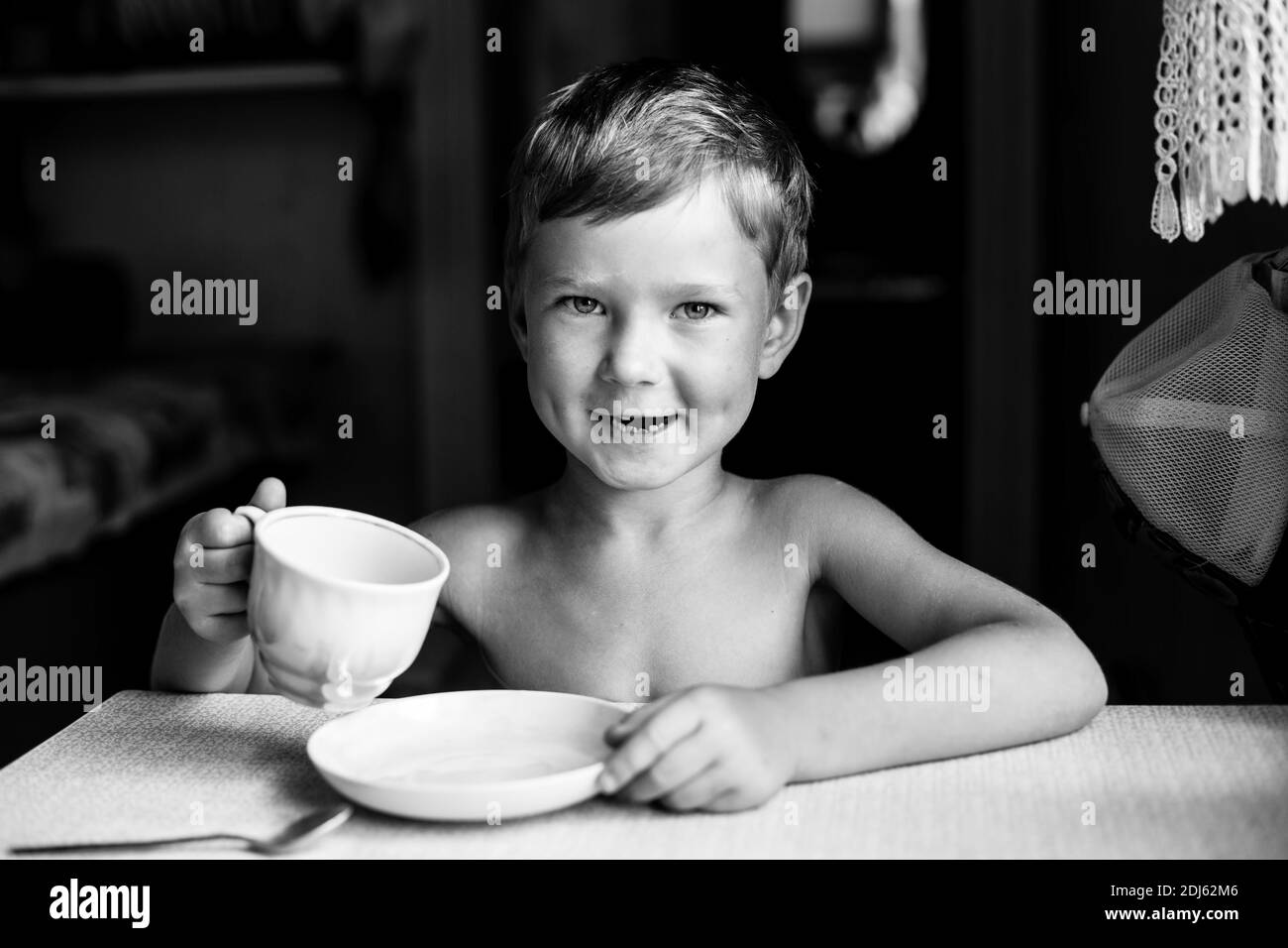 Little boy is drinking tea at the table at home. Black and white photo ...