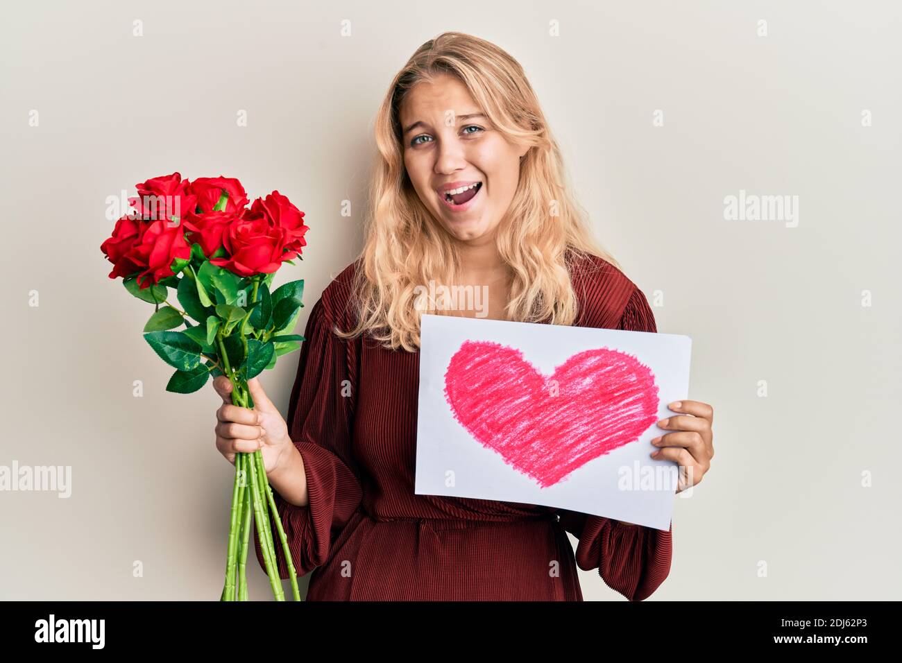 Young blonde girl holding heart draw and bouquet of roses celebrating ...