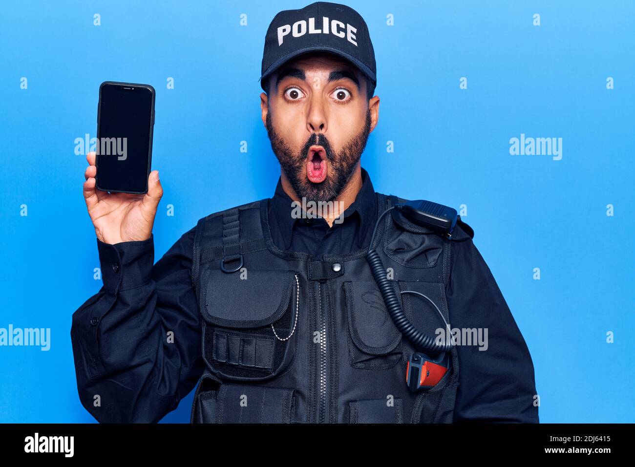 Young hispanic man wearing police uniform holding smartphone scared and ...