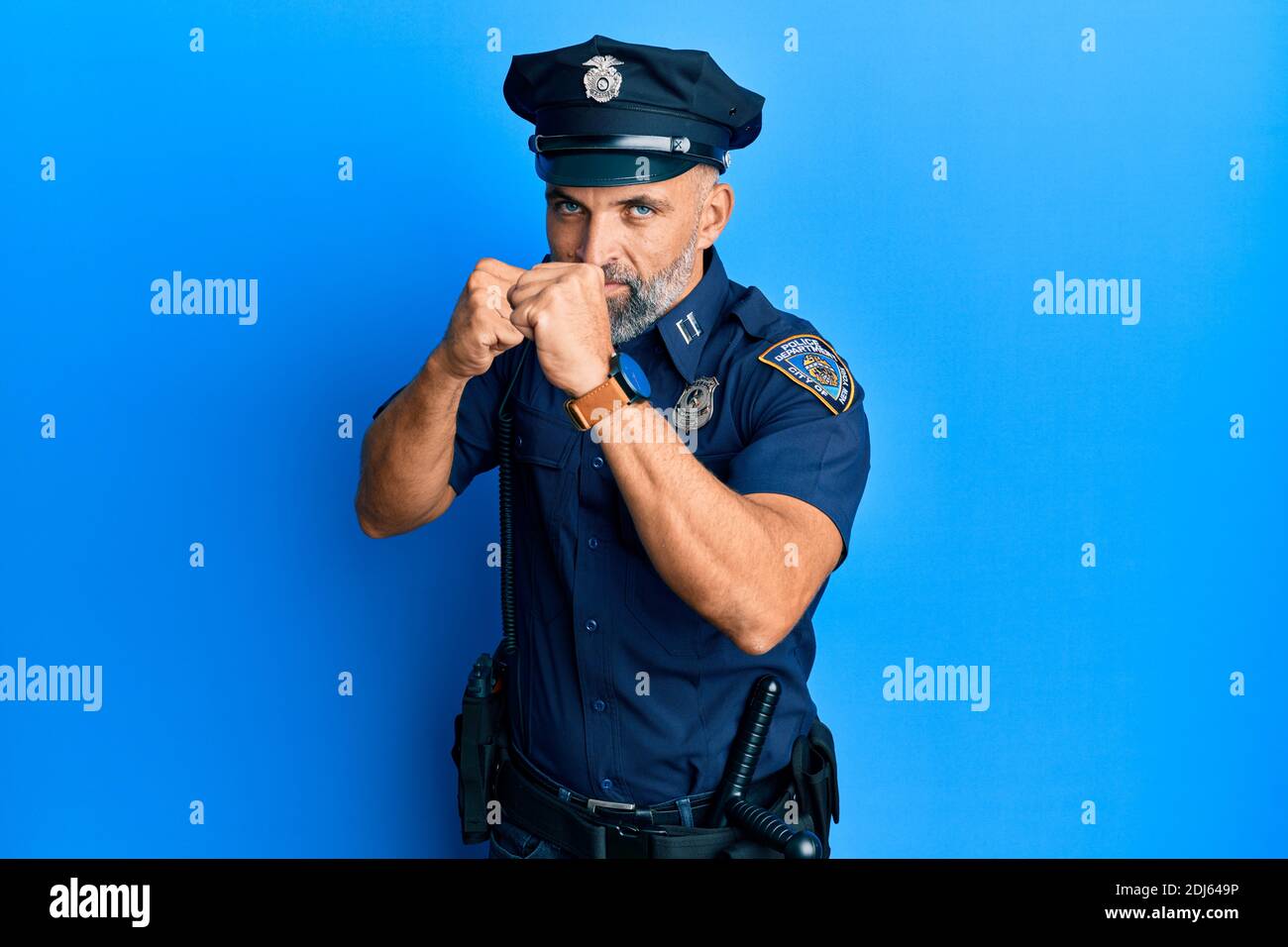 Middle age handsome man wearing police uniform ready to fight with fist ...