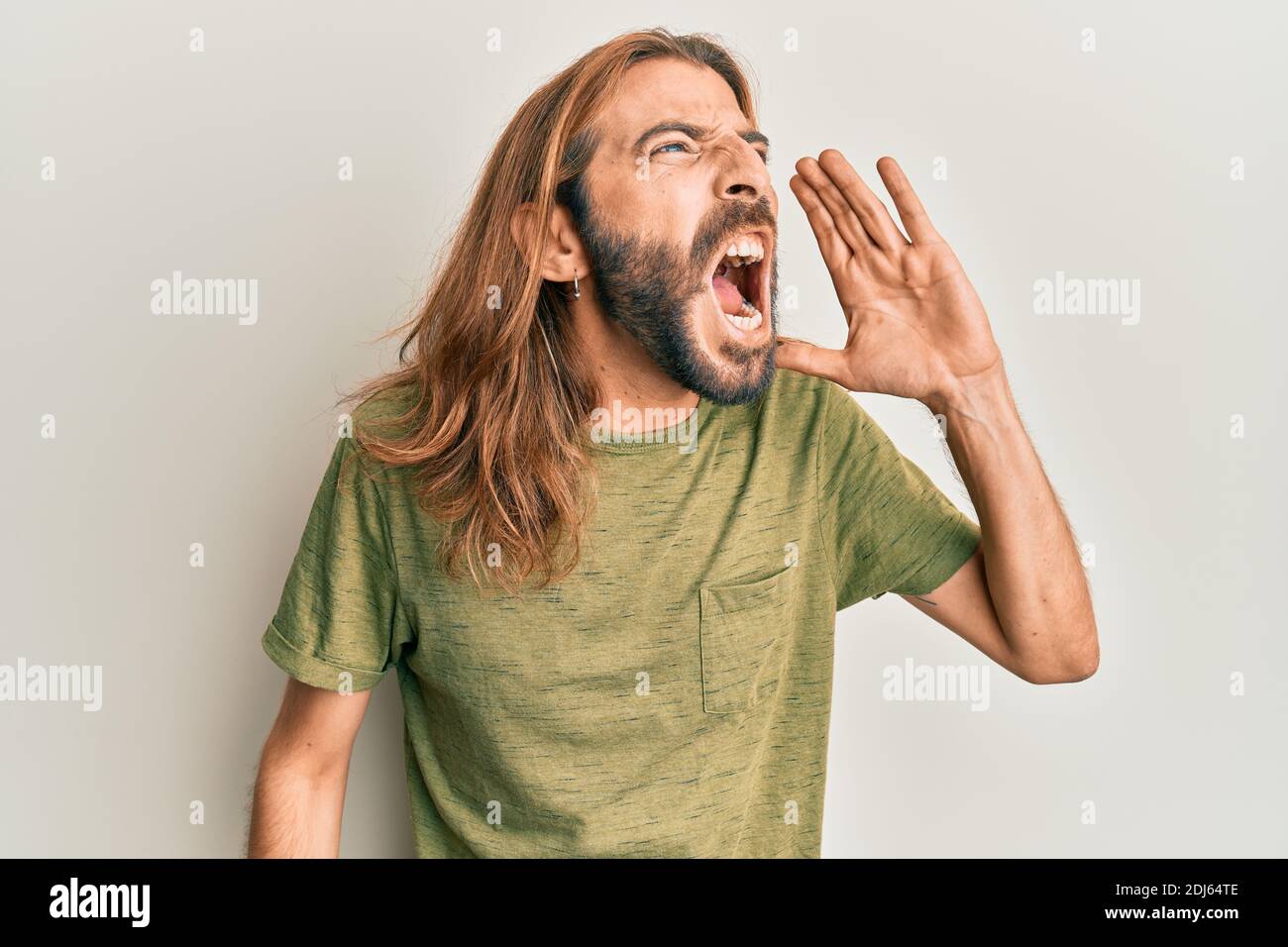 Attractive man with long hair and beard wearing casual clothes shouting ...
