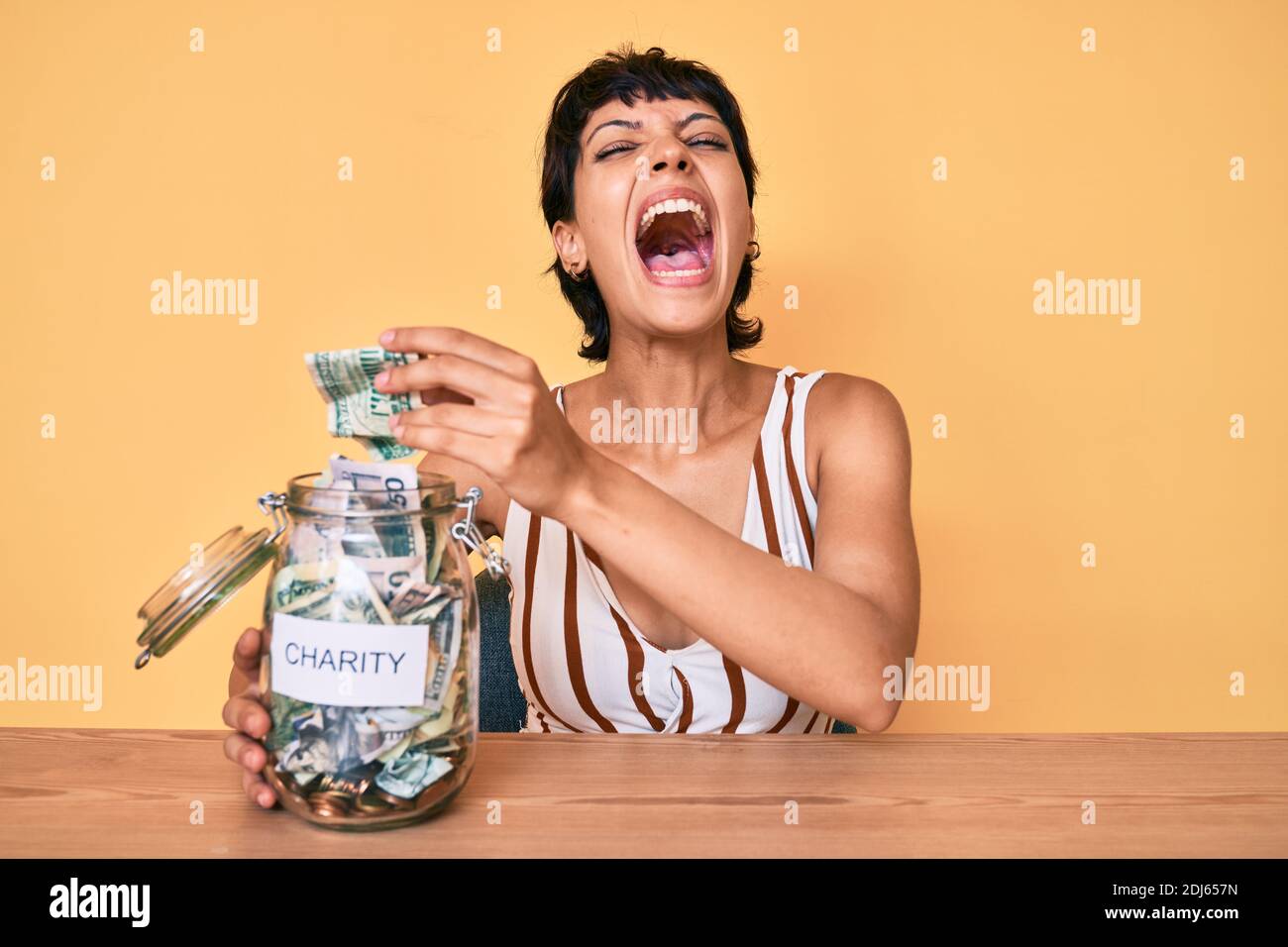 Beautiful brunettte woman holding charity jar with money angry and mad ...