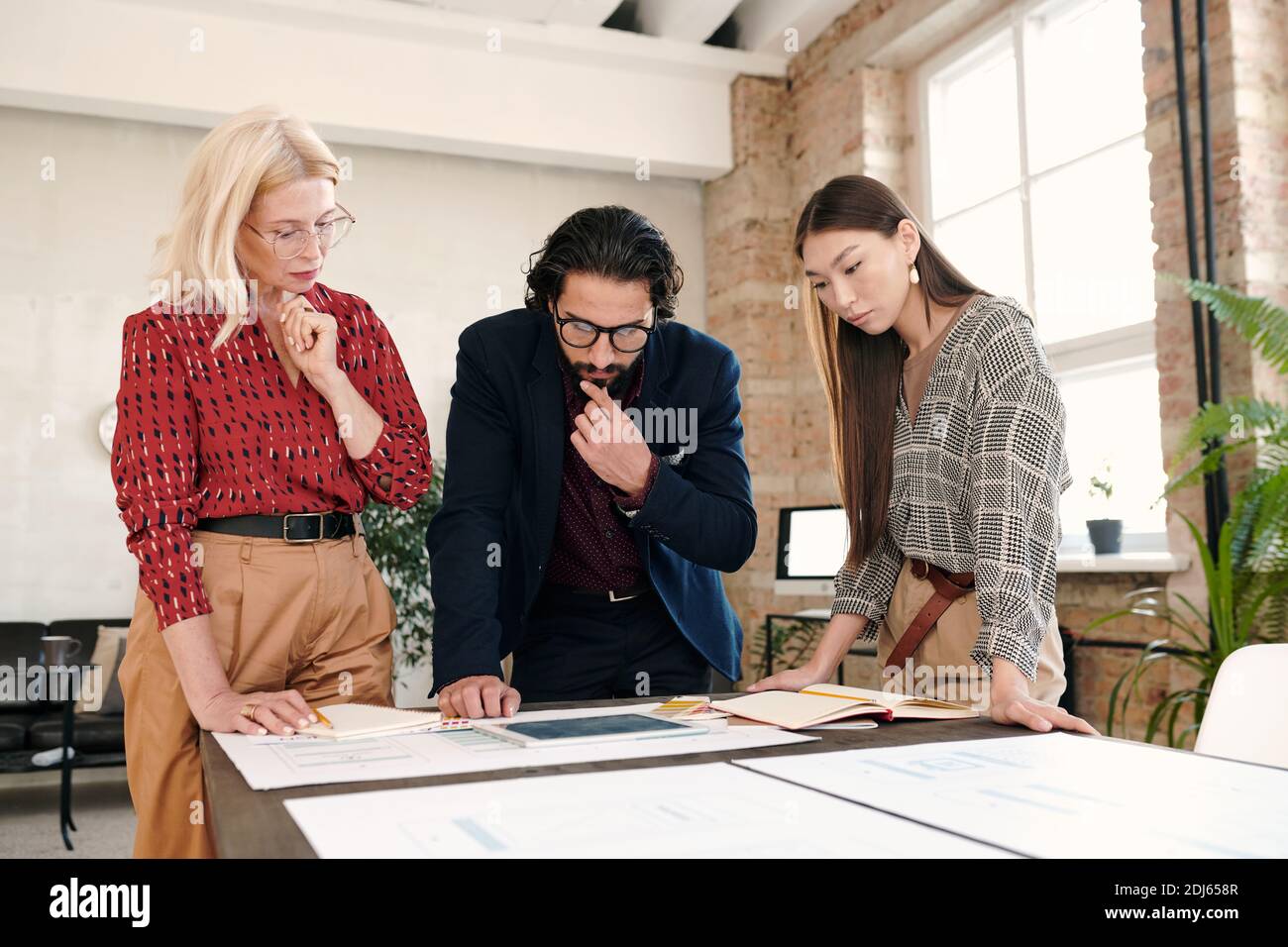 Three pensive intercultural mobile application developers standing by ...