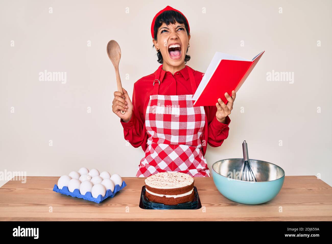 Beautiful brunettte woman cooking cake reading recipes book angry and ...