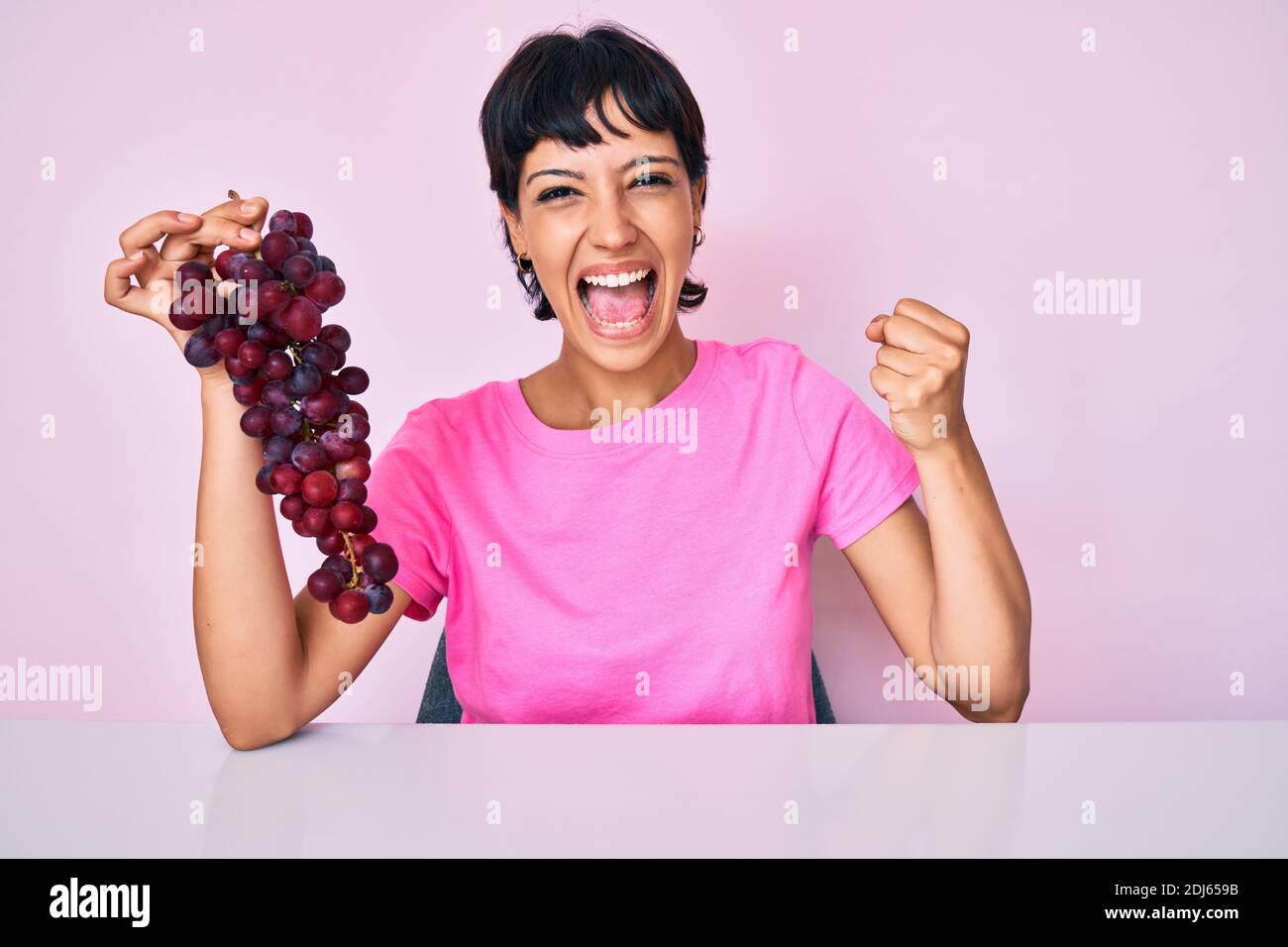 Beautiful brunettte woman holding branch of fresh grapes screaming ...