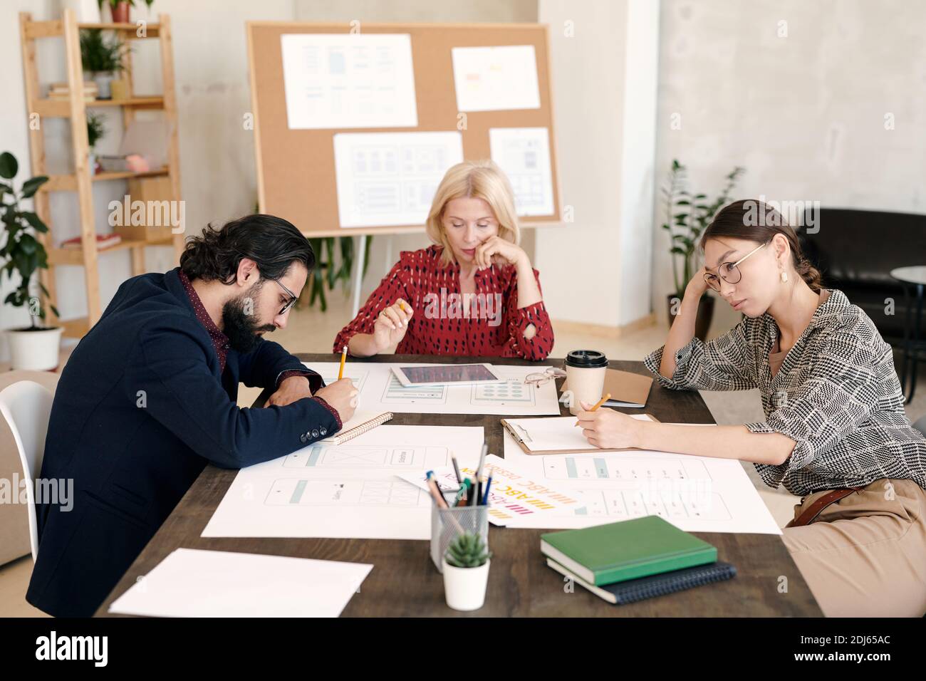 Three pensive colleagues sitting by table and brainstorming while ...