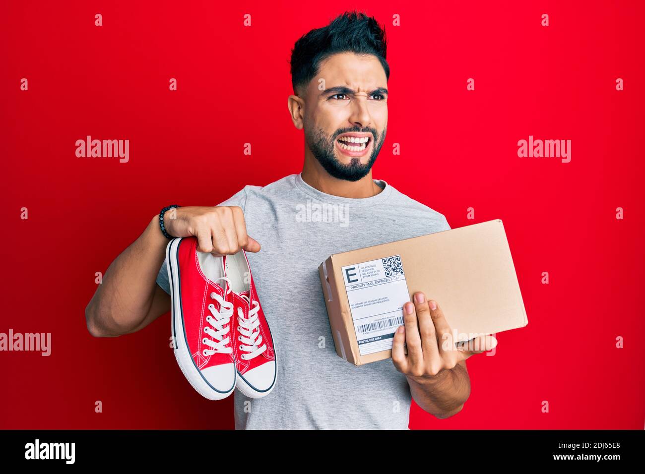 Young man with beard taking casual red shoes from box angry and mad ...