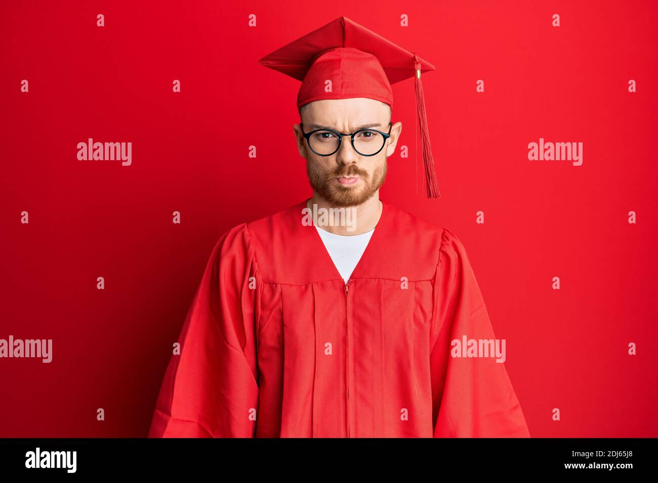 Young redhead man wearing red graduation cap and ceremony robe ...