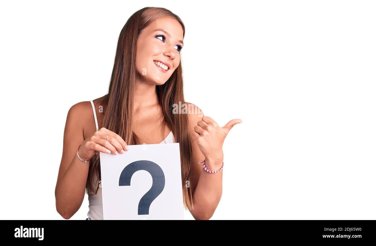Young beautiful hispanic woman holding question mark pointing thumb up ...