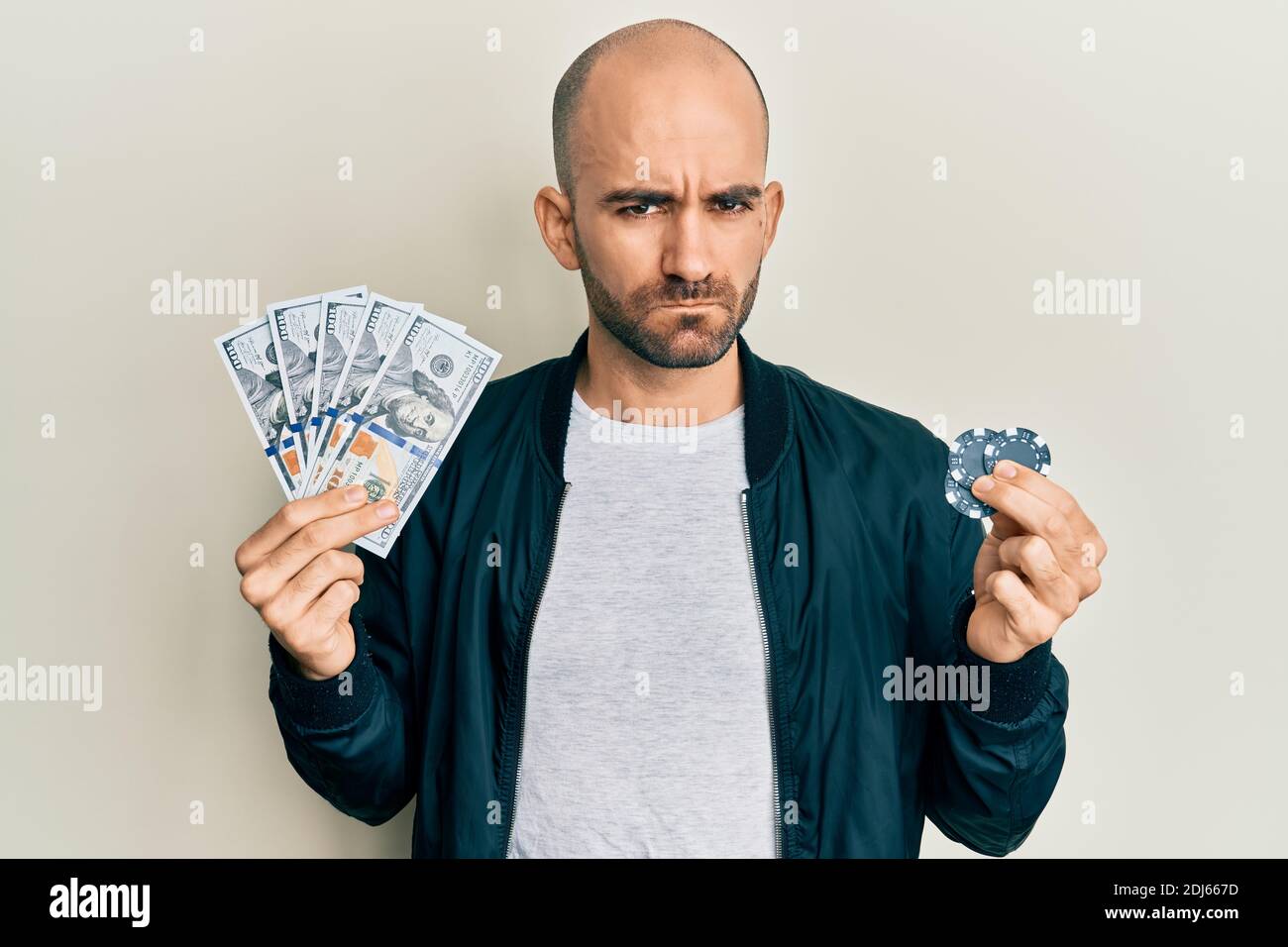 Young hispanic man playing poker holding dollars banknotes and chips ...