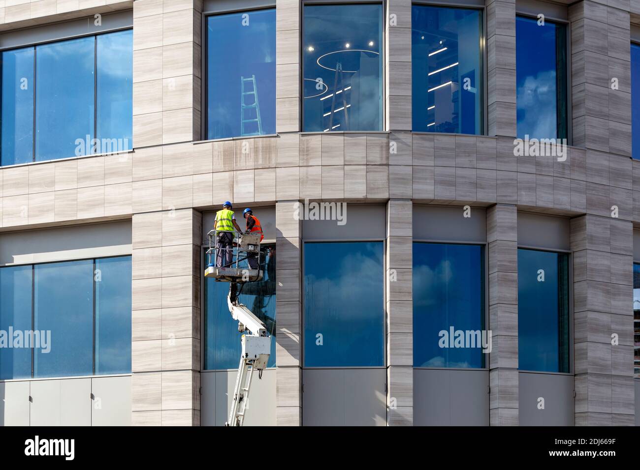 Workers in elevated platform cleaning building facade window glass by ...