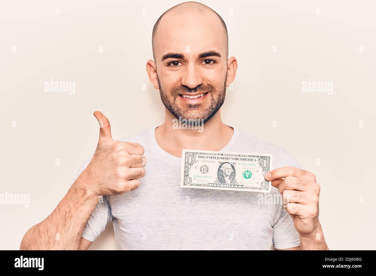 Young handsome bald man holding one dollar banknote smiling happy and ...