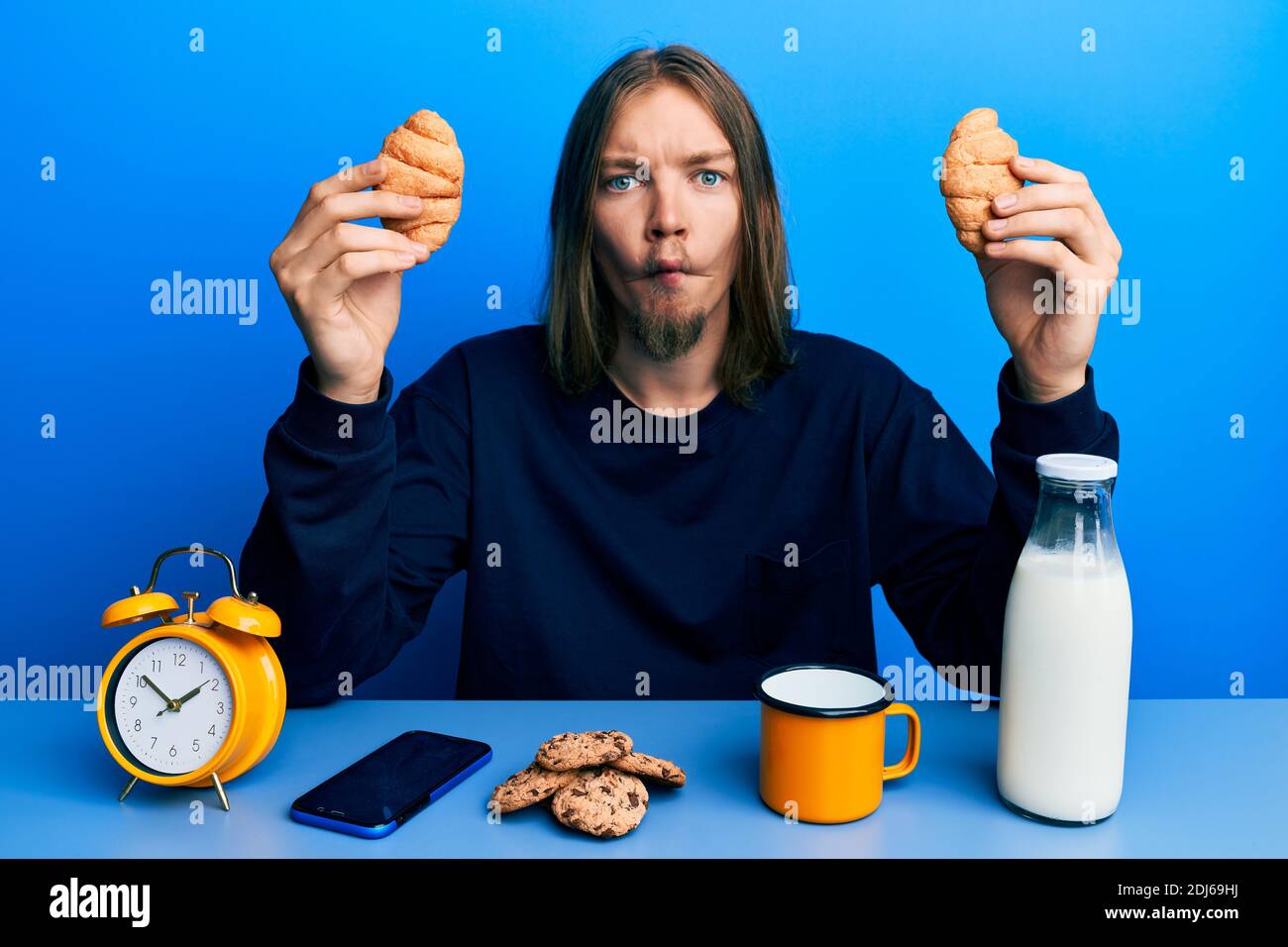 Handsome caucasian man with long hair eating croissant for breakfast ...