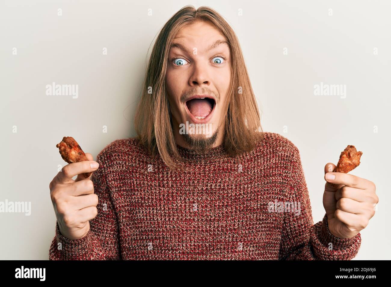 Handsome caucasian man with long hair eating chicken wings celebrating ...