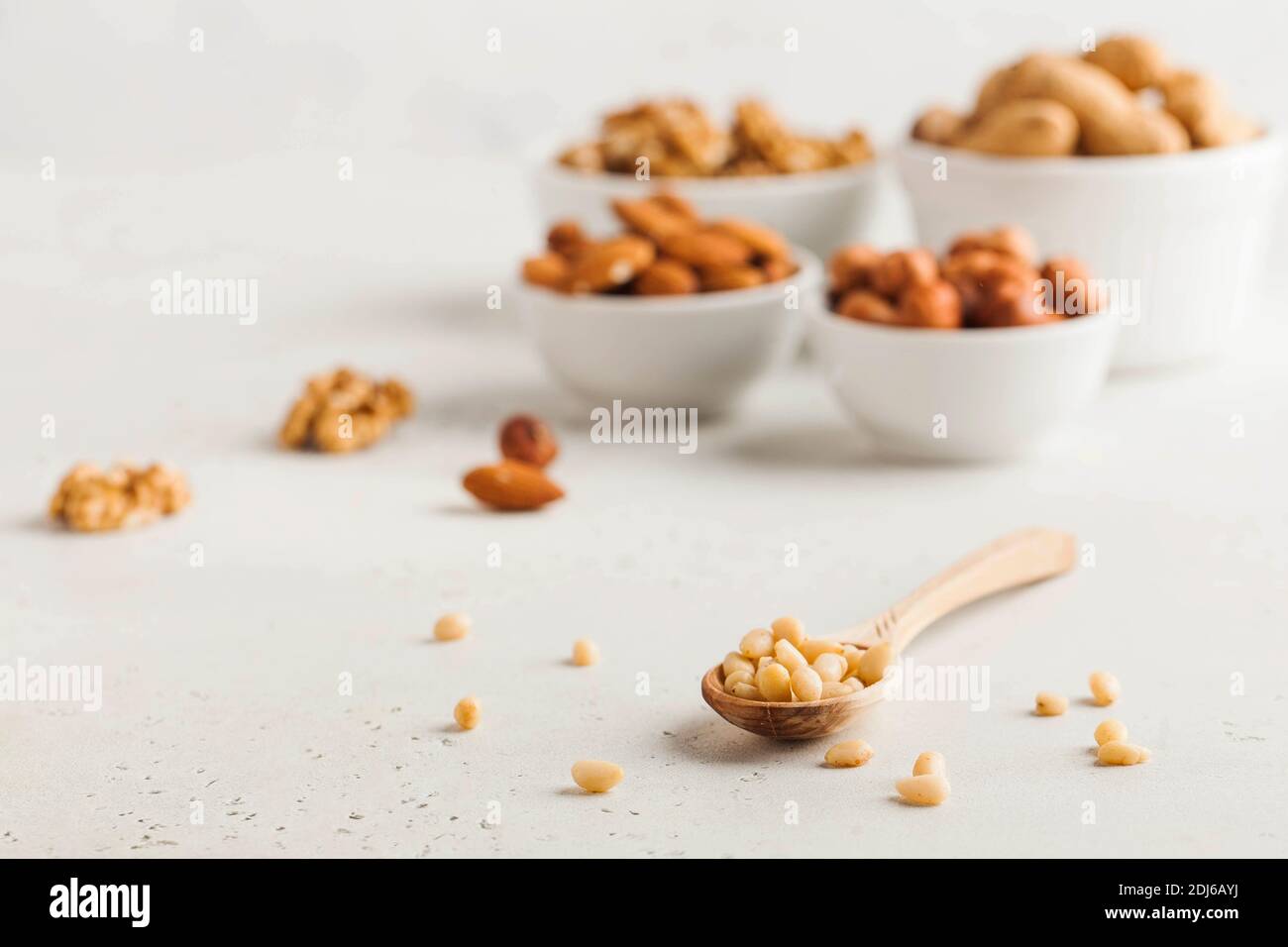 A handful of pine nuts in a wooden spoonl, assorted nuts on a light ...