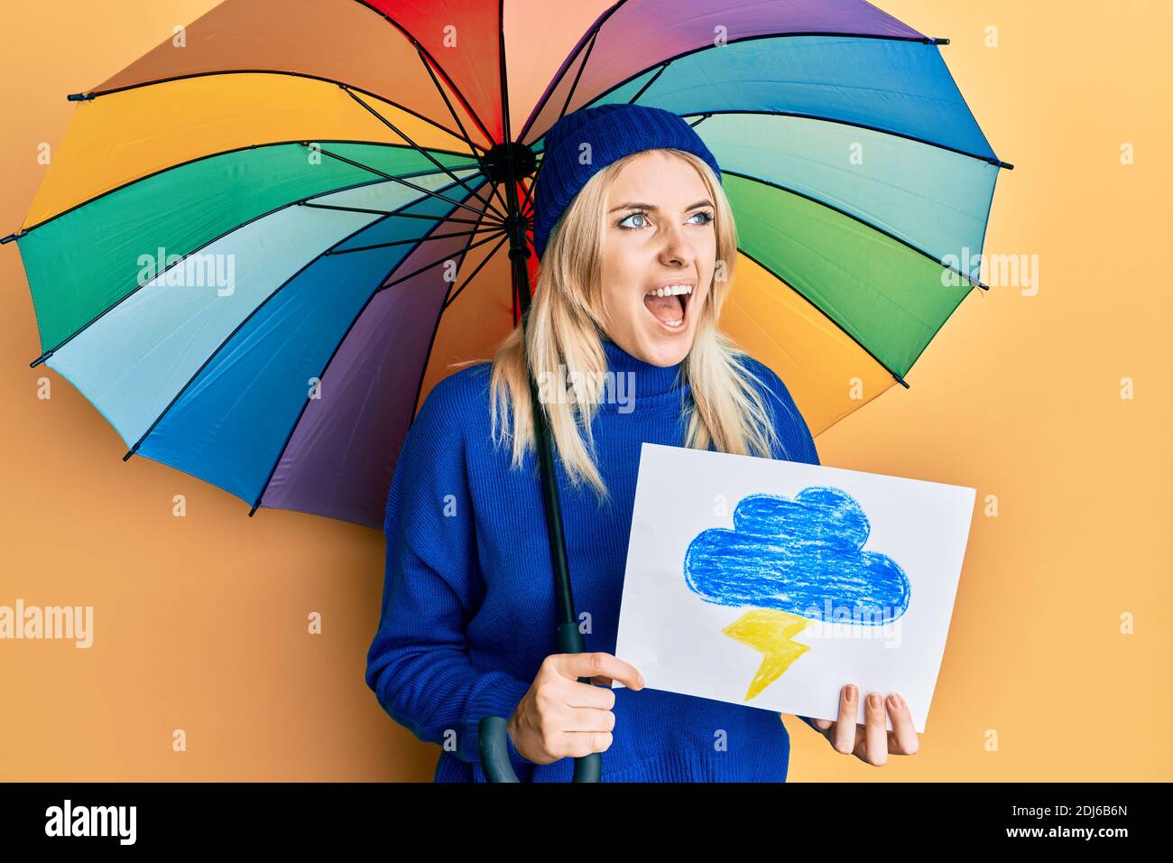 Young caucasian woman holding rain draw and umbrella angry and mad ...