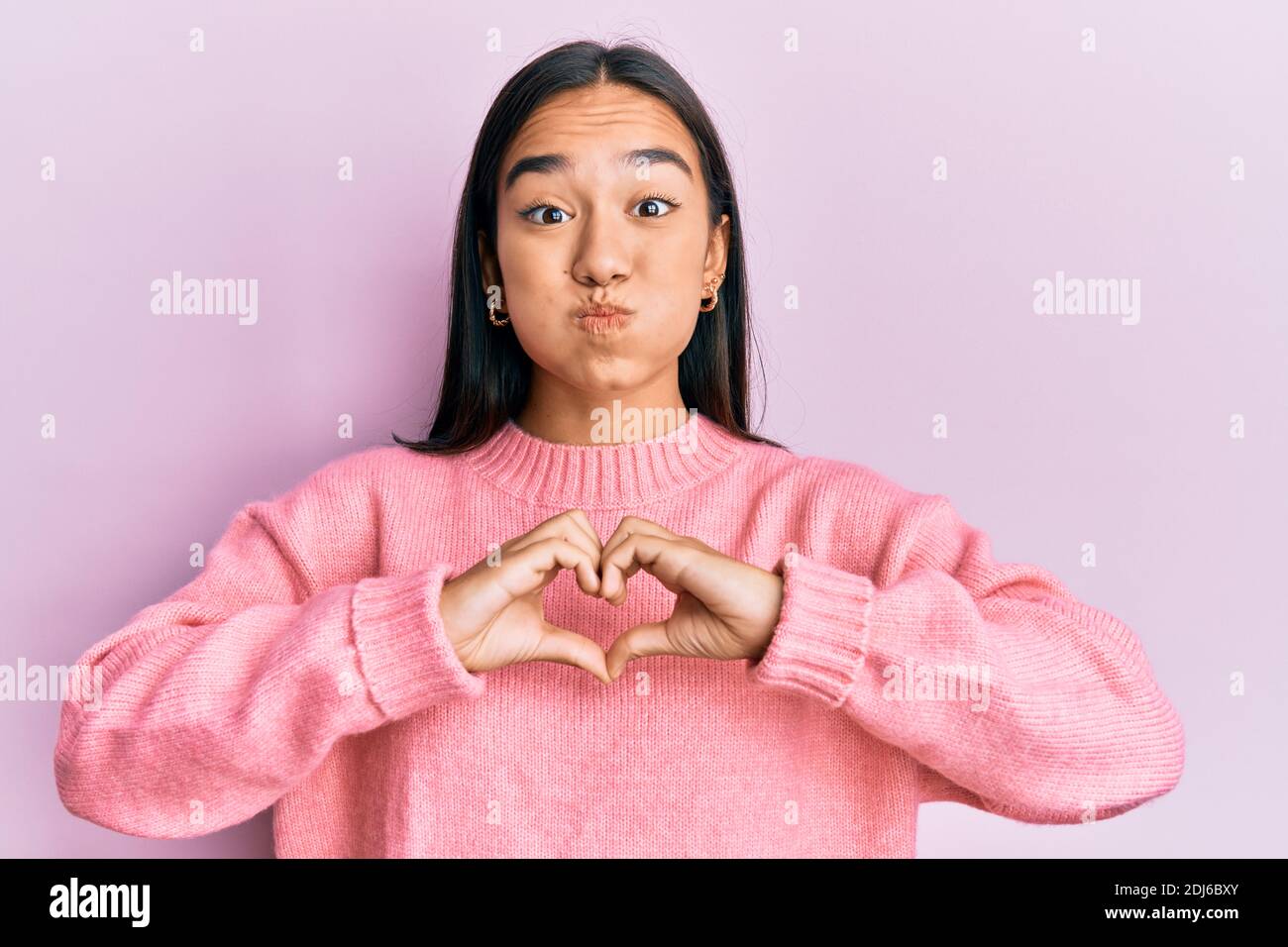 Young asian woman doing heart symbol with hands puffing cheeks with ...
