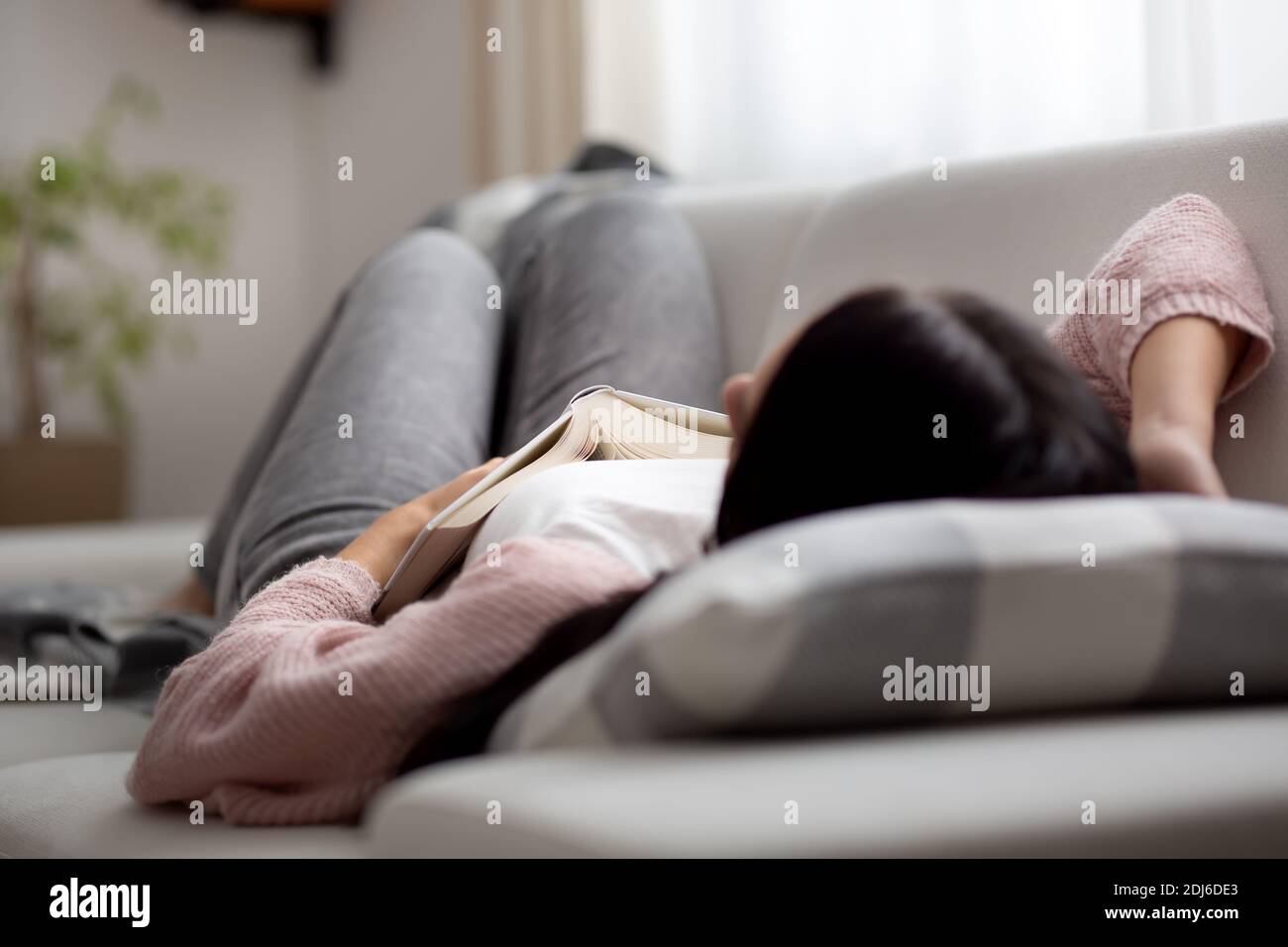 A woman falling asleep during the day on a couch while trying to read a ...