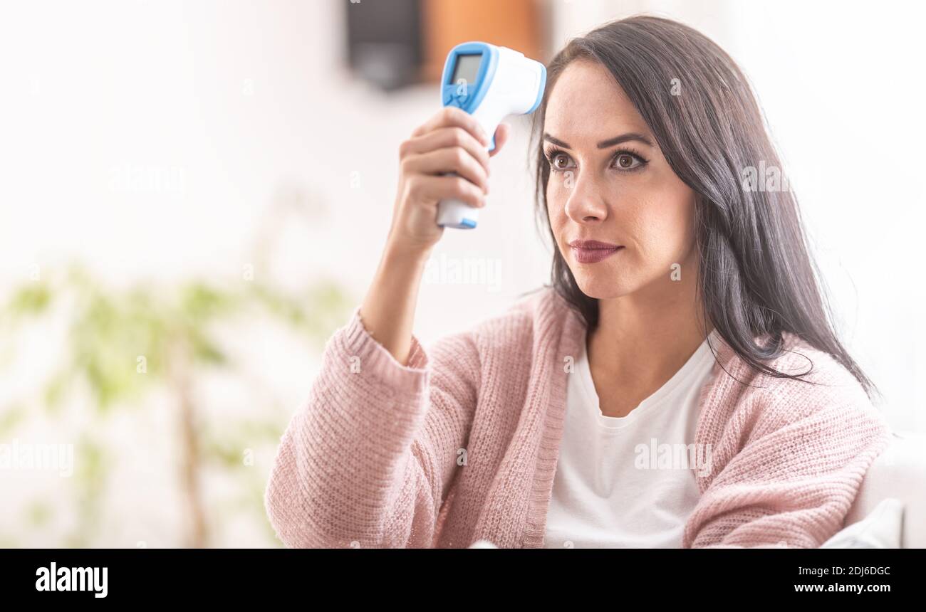 Woman self-measuring temperature with an infrared digital thermometer ...