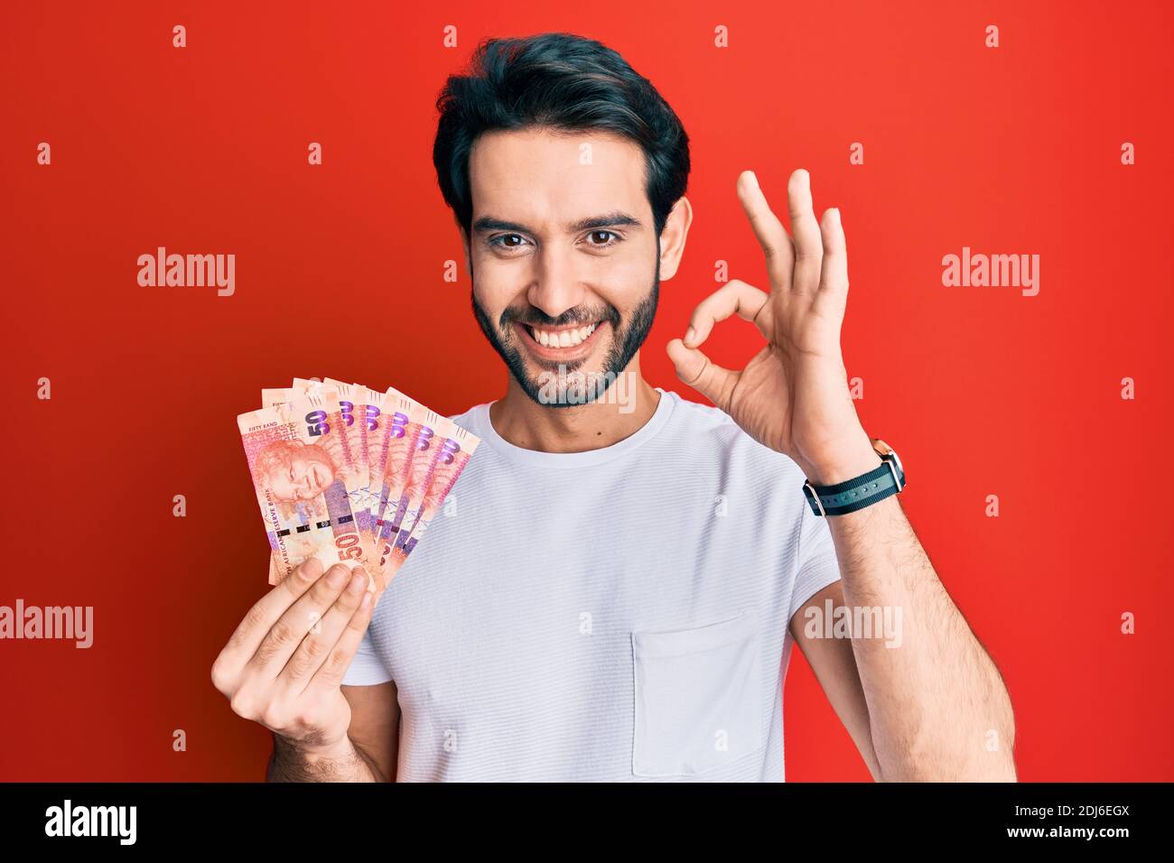 Young hispanic man holding south african rand banknotes doing ok sign ...