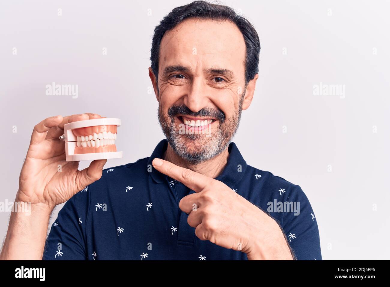 Middle age handsome man holding denture showing teeth over isolated ...