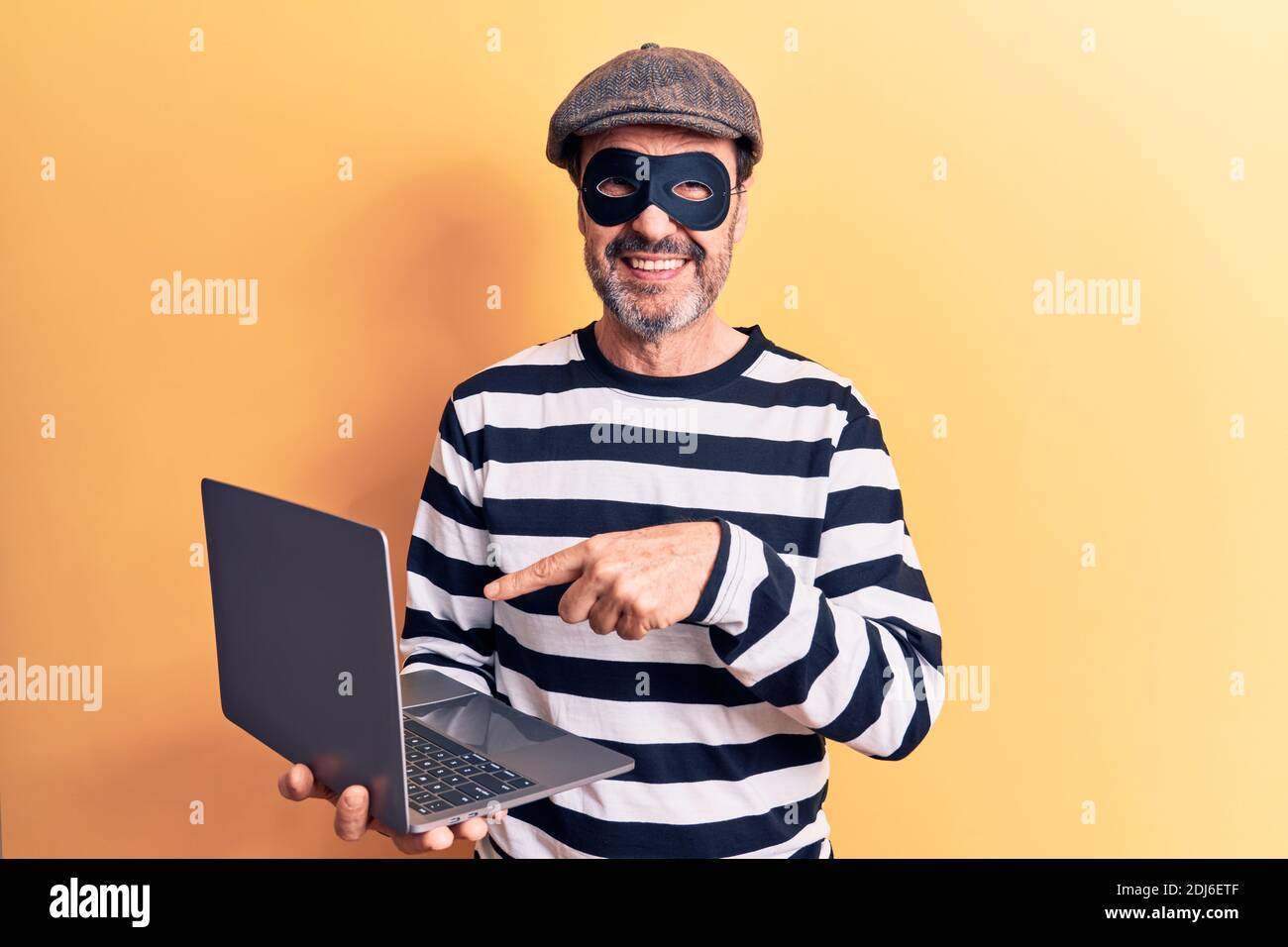 Middle age handsome burglar man wearing cap and mask using laptop over ...