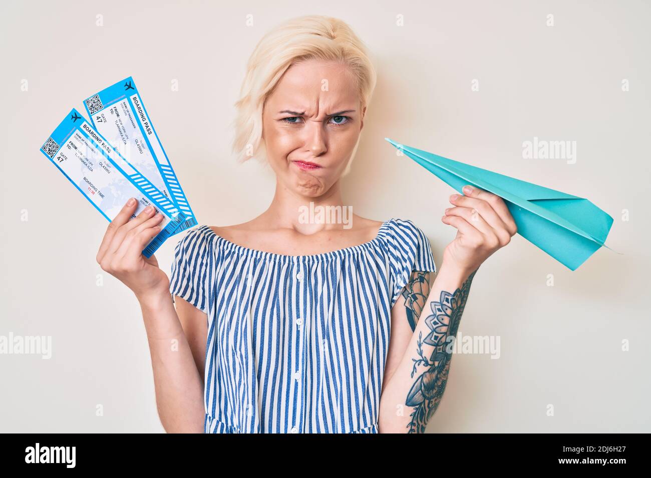 Young blonde woman with tattoo holding paper airplane and boarding pass ...