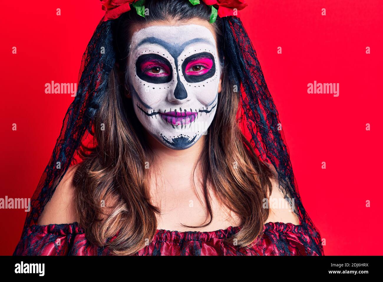 Young woman wearing day of the dead costume over red with a happy and ...