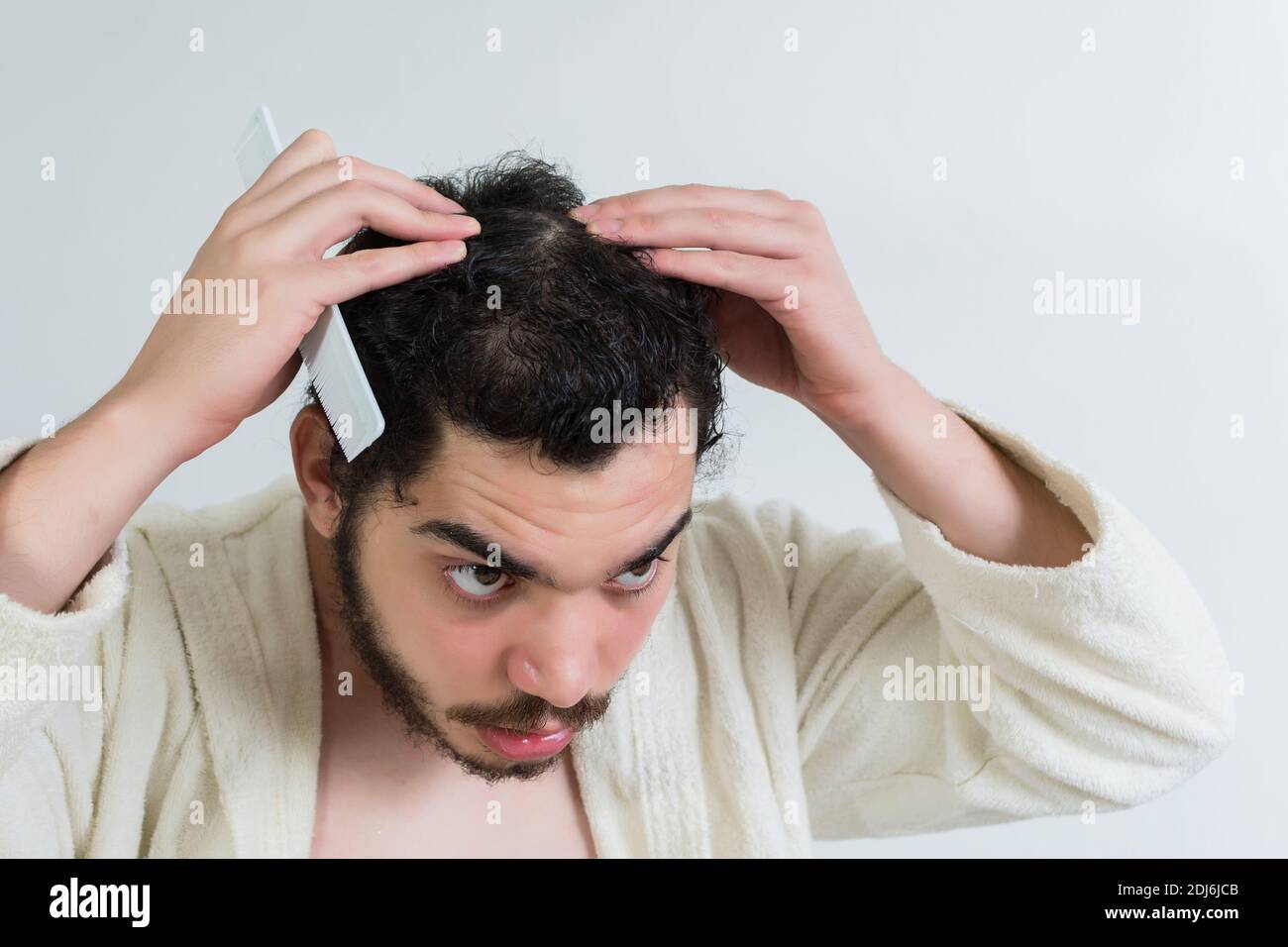 A caucasian male worried about hair loss and looking in the mirror at ...