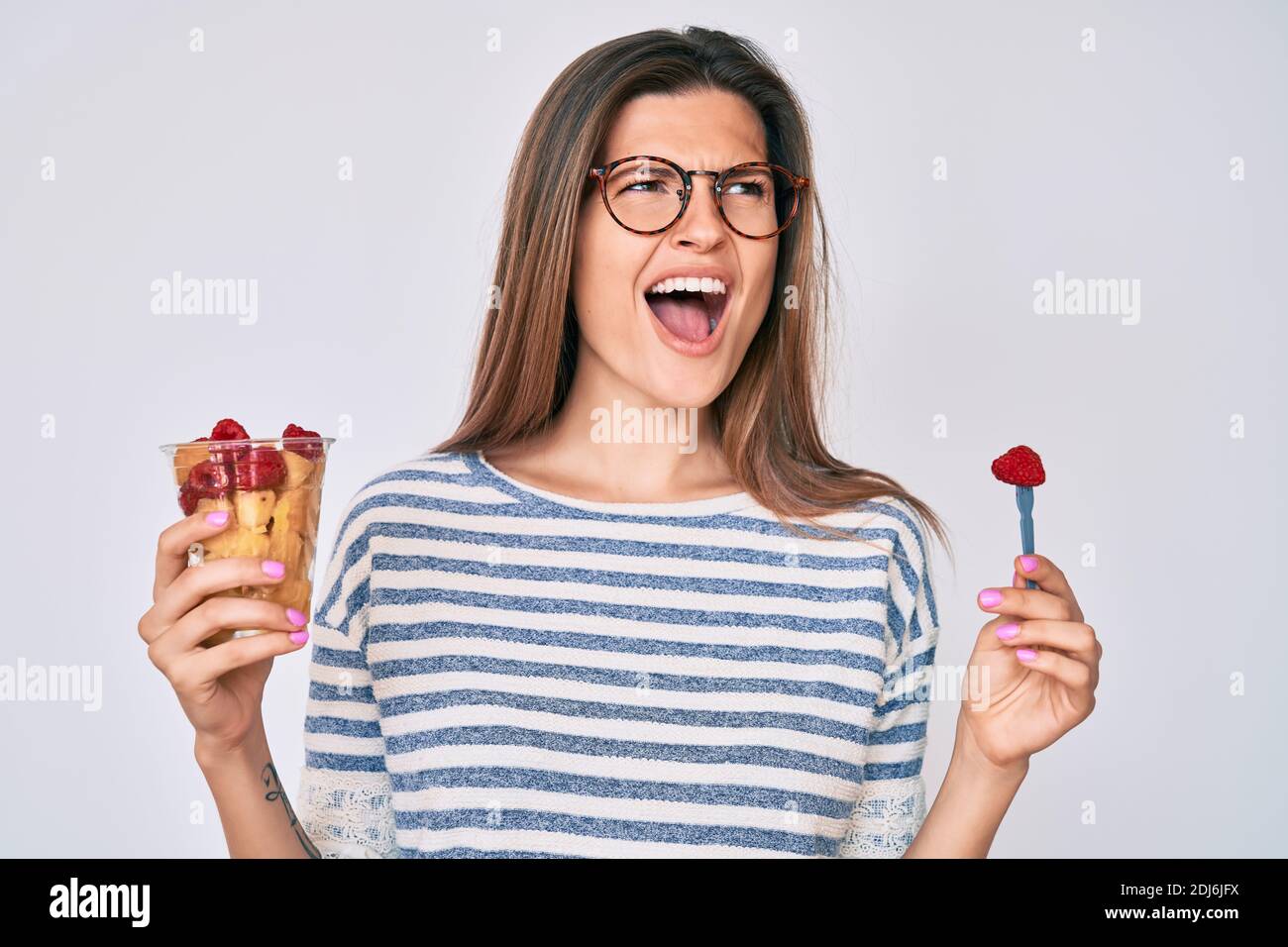 Beautiful caucasian woman eating fresh and healthy fruit angry and mad ...