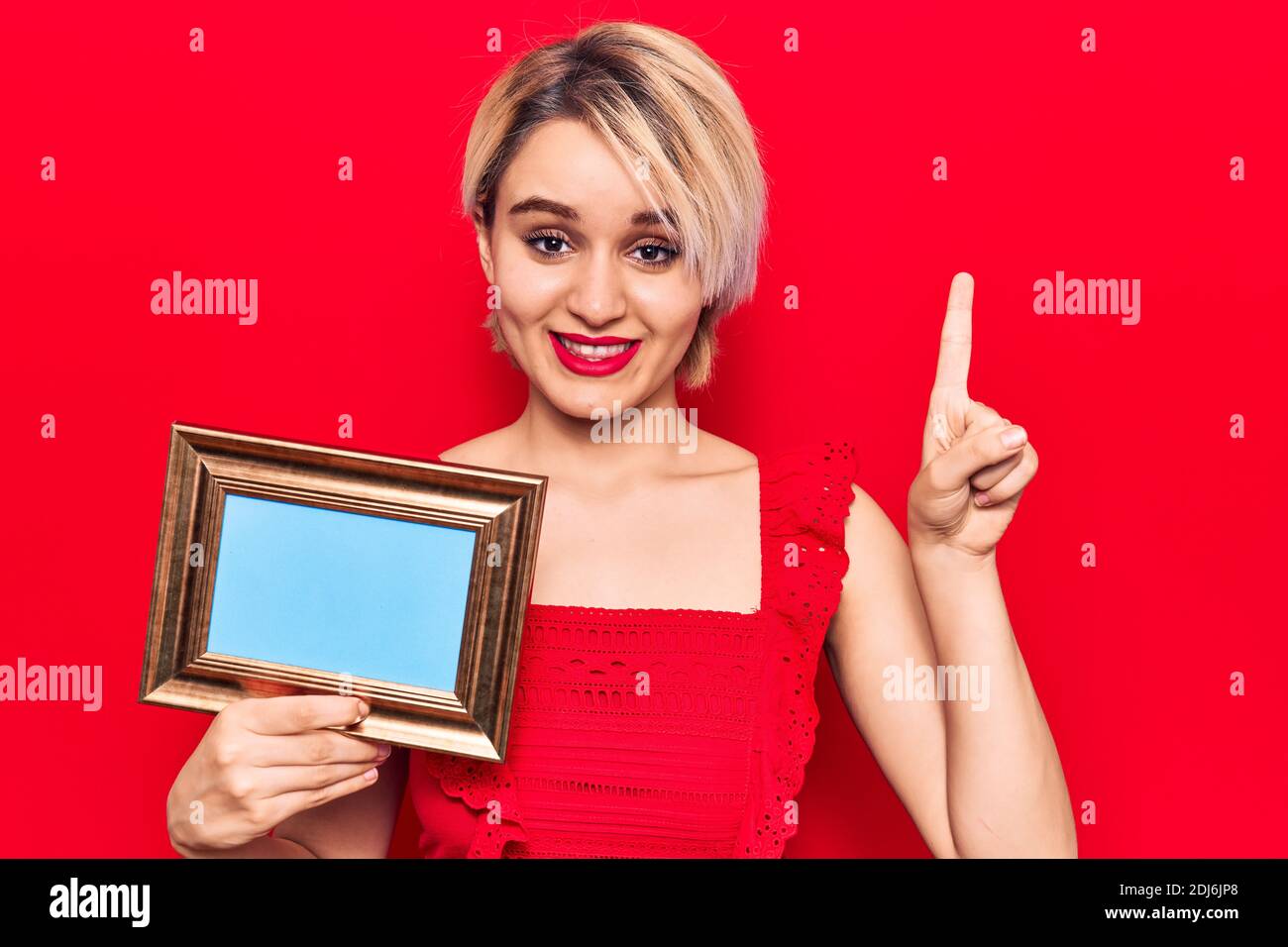 Young beautiful blonde woman holding empty frame smiling with an idea ...
