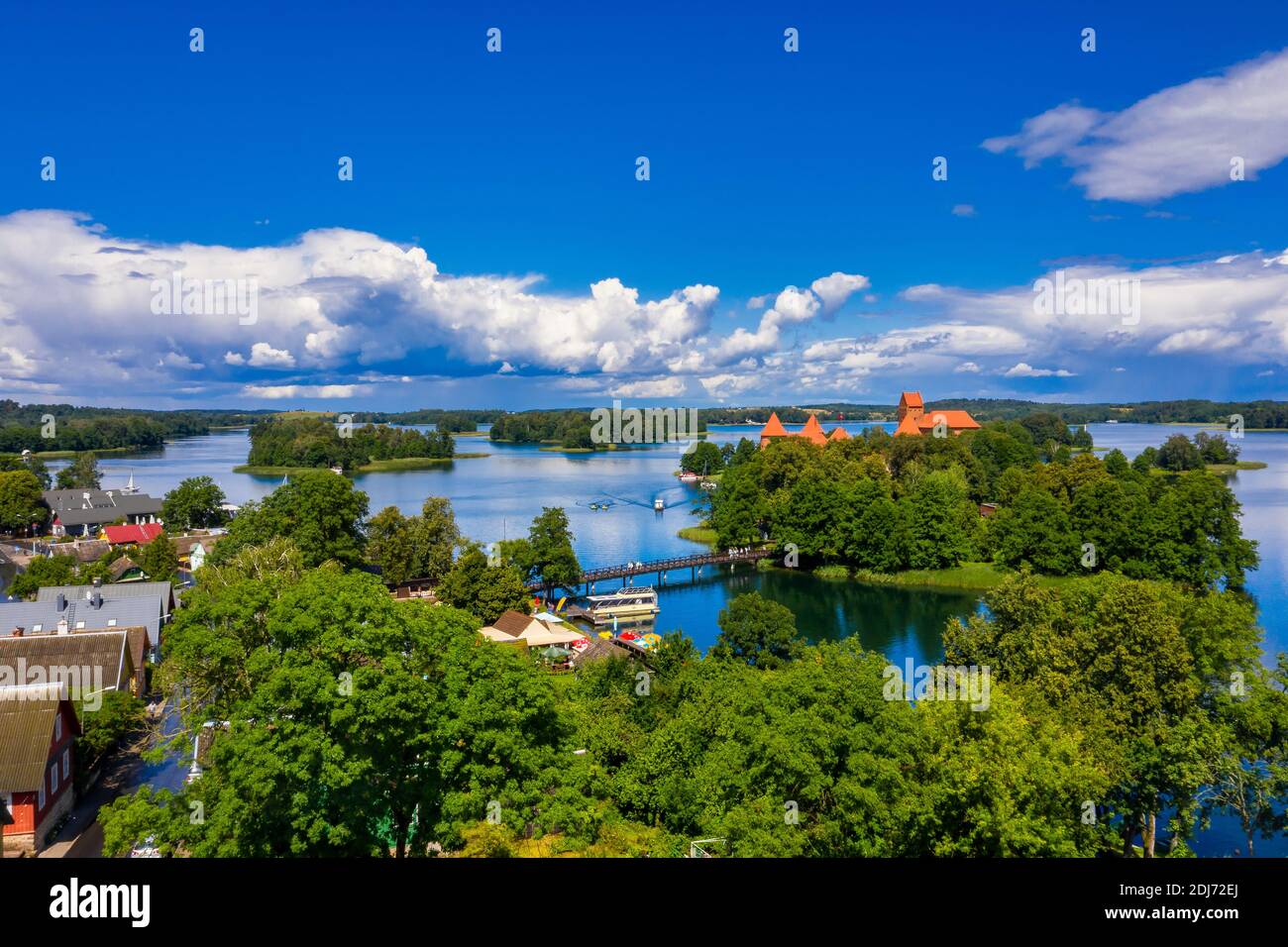 A landscape of Trakai surrounded by greenery and sea under a blue sky ...