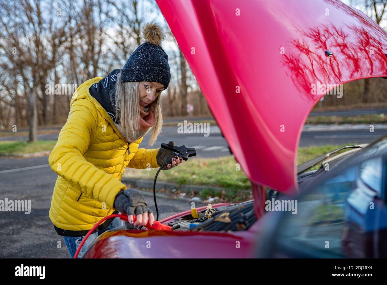 Beautiful blonde woman in yellow jacket trying to start her broken car ...