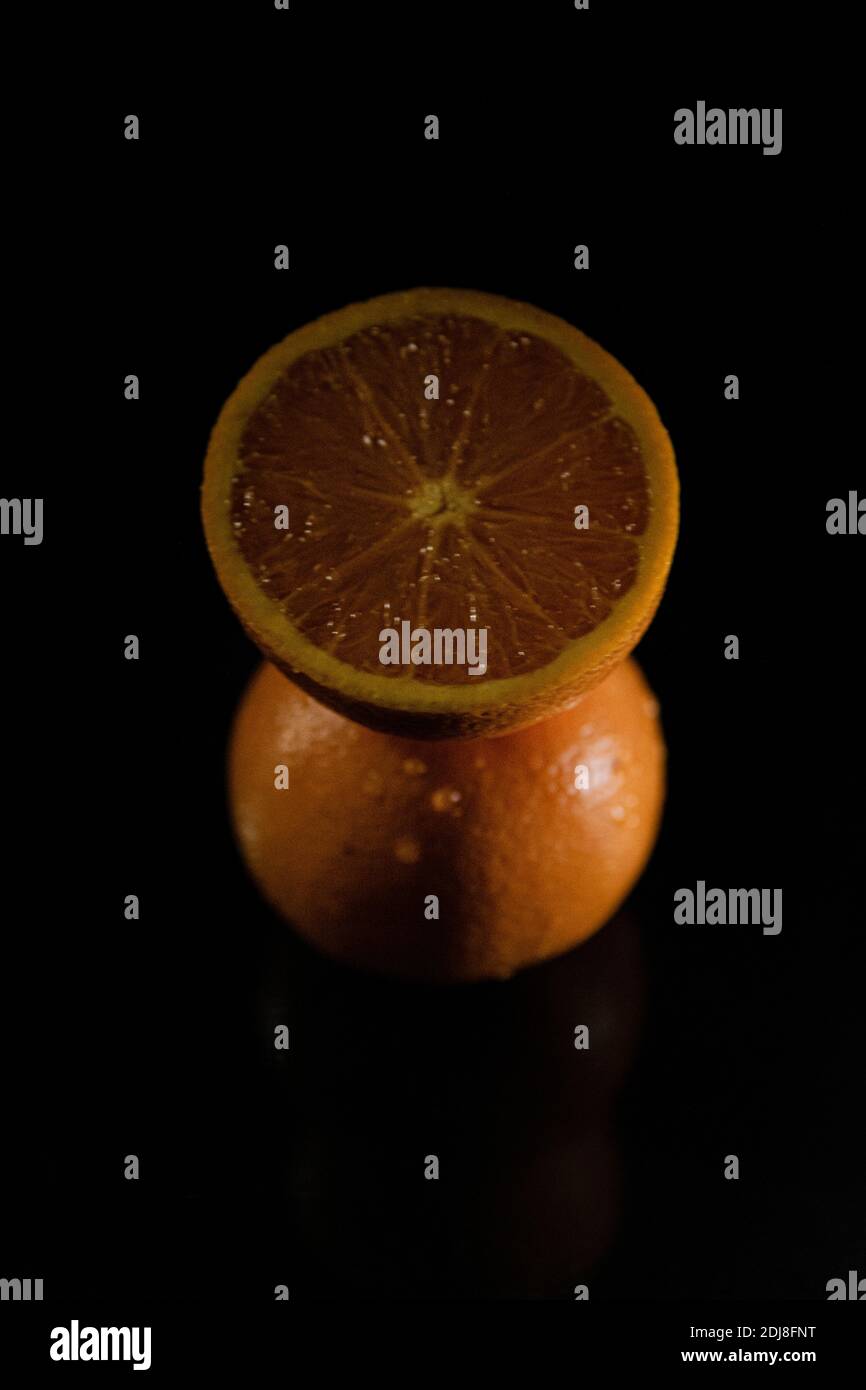 A vertical shot of a cut wet orange and a slice isolated on black ...