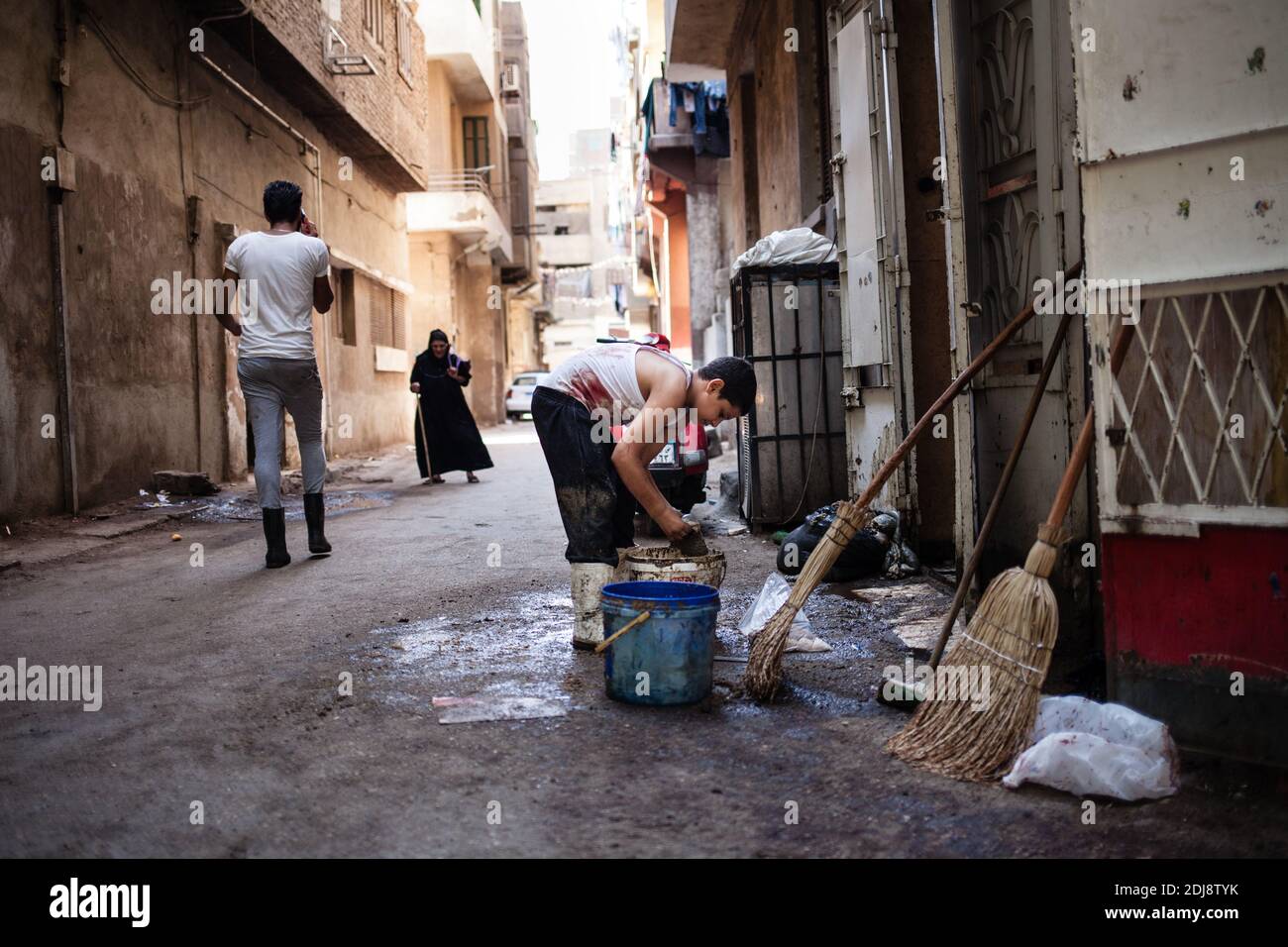A young man is cleaning tools in the street behind the butchery ...