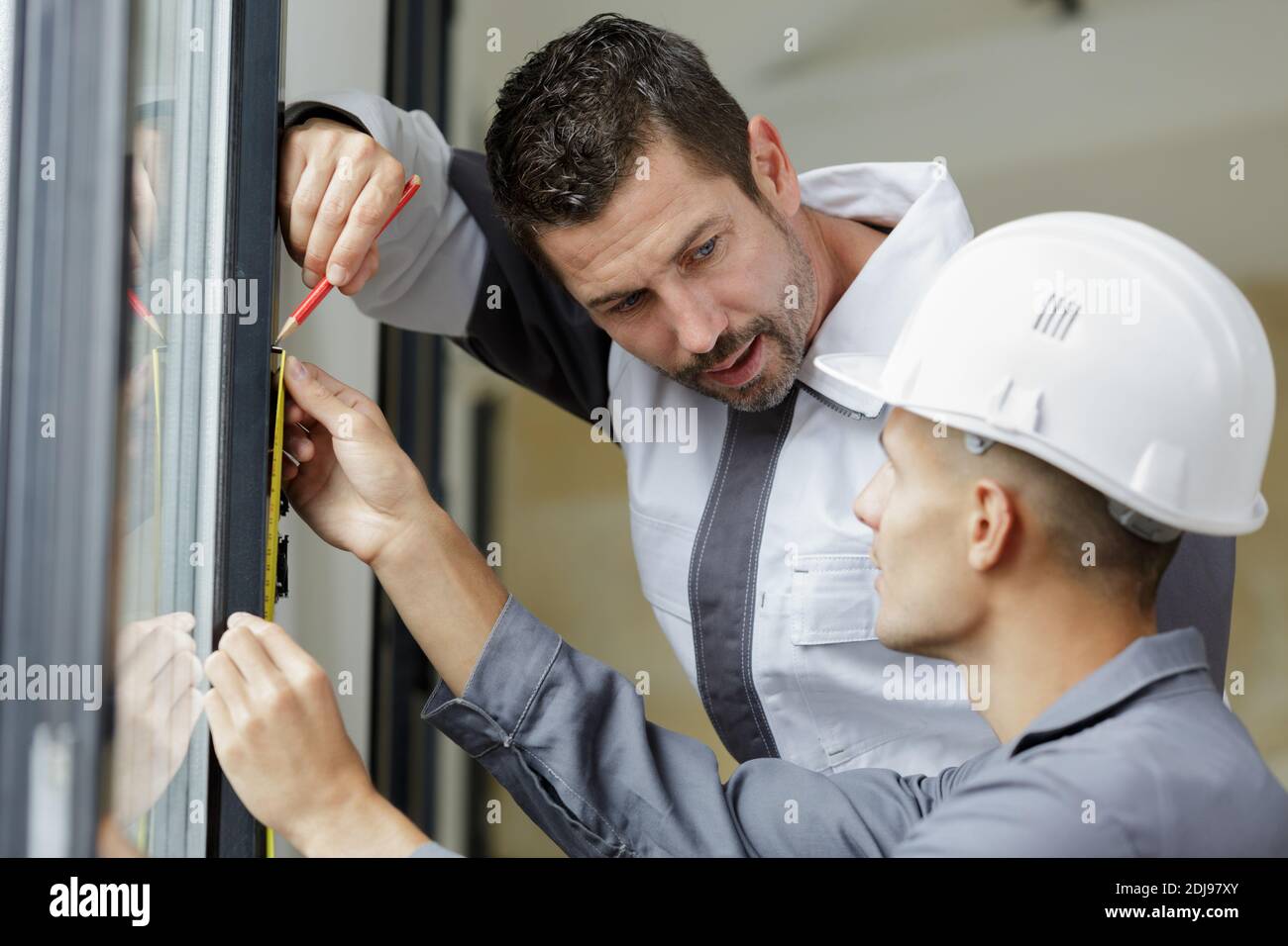 supervisor watching apprentice mark position on window frame Stock ...