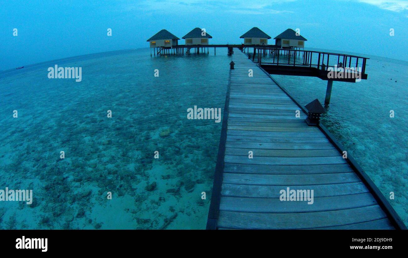 The view of a long pier and wooden huts in Maldives before sunrise ...