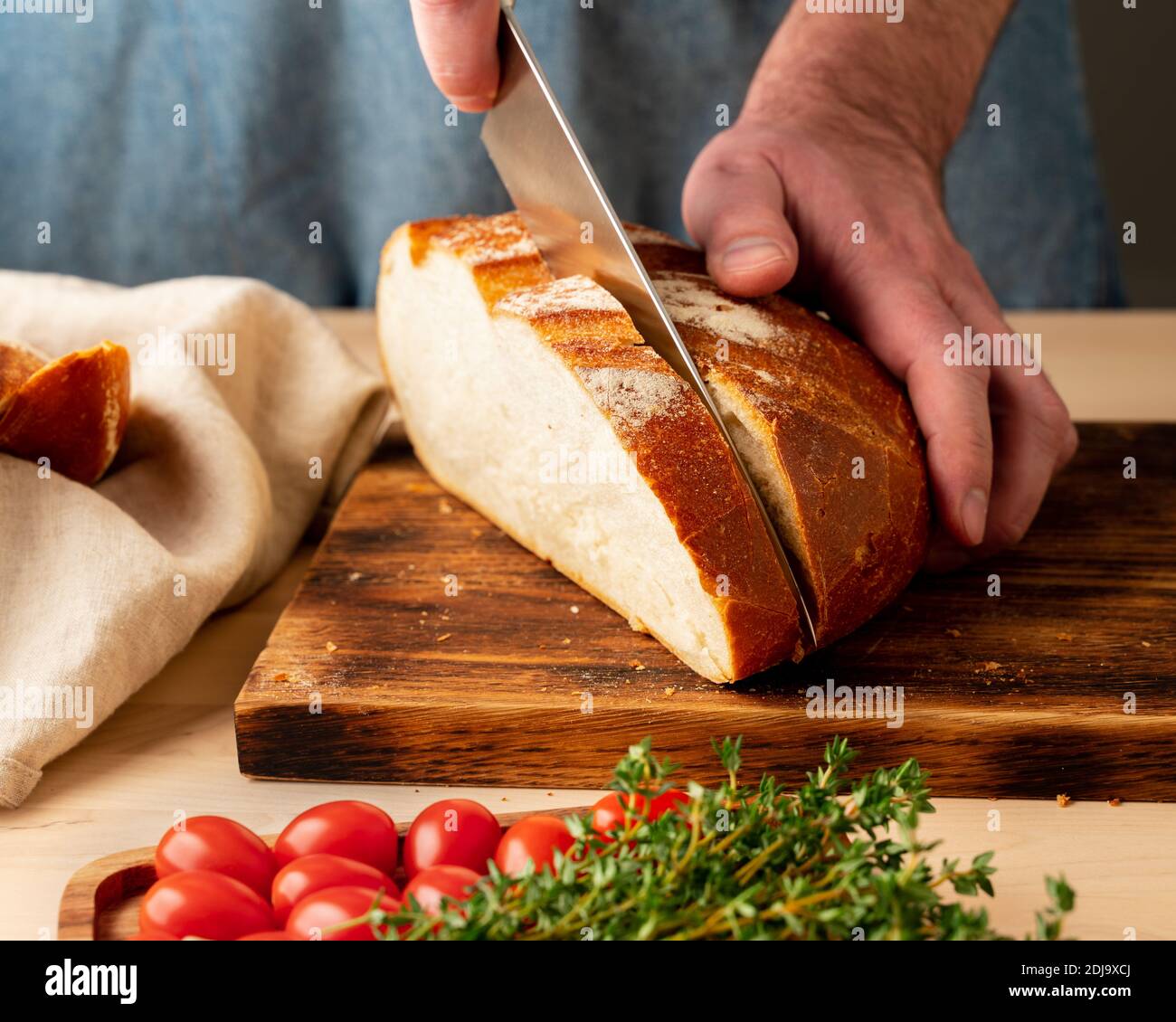 Faceless man cutting fresh home-baked crusty bread with large knife ...