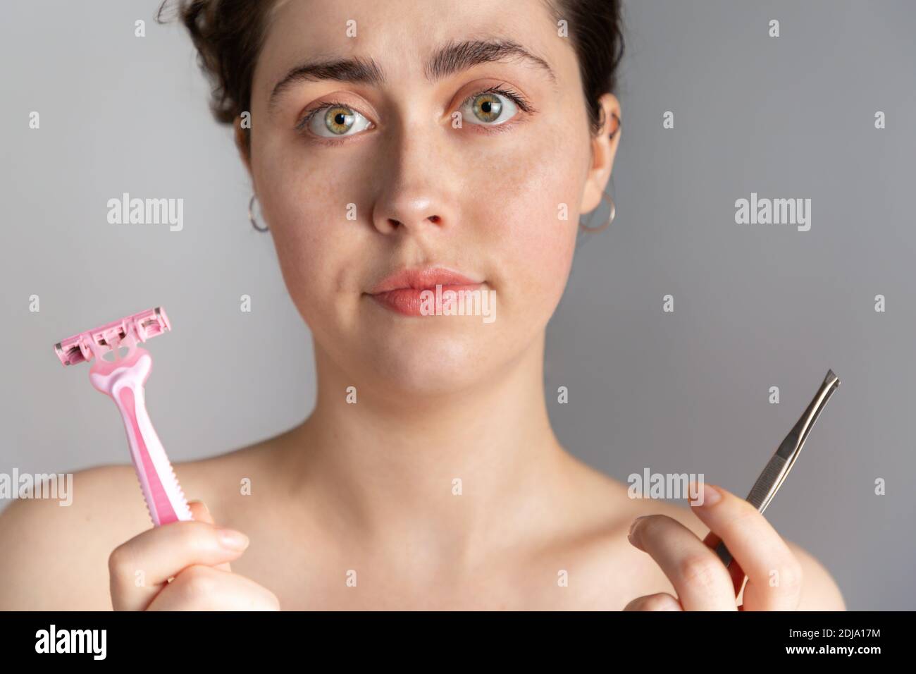 A young pretty woman holding a pair of tweezers and a razor, not ...