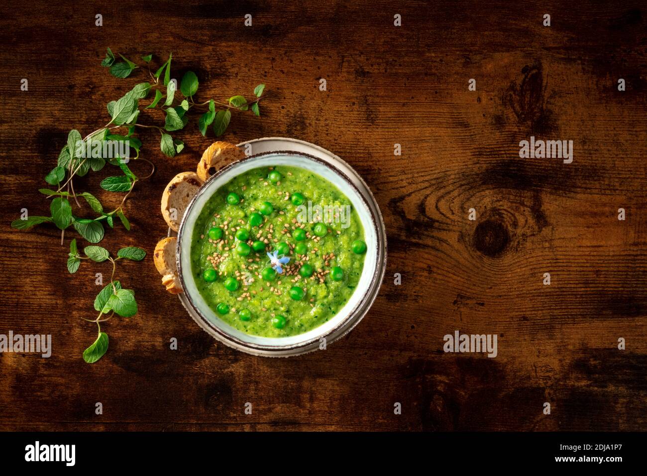 Vegan green soup, shot from above with toasts and mint on a dark rustic ...