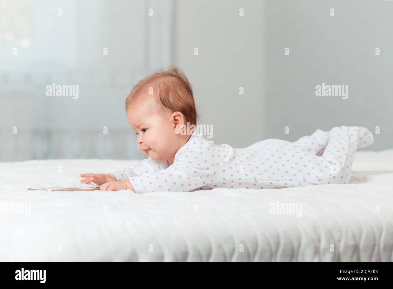A toddler in sliders is lying on the bed and playing with a smartphone ...