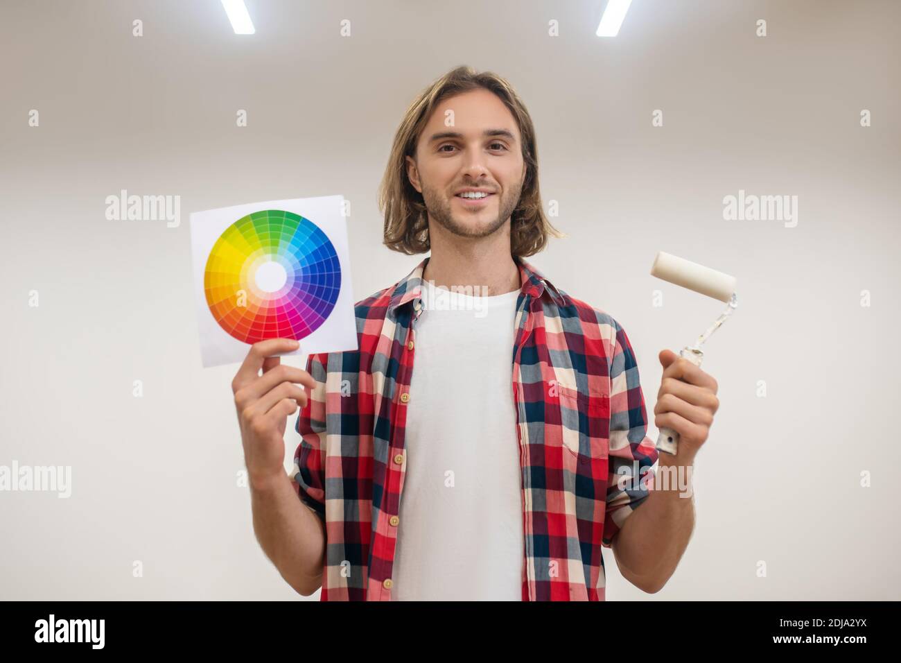 Young man holding a paint roller and a color palette Stock Photo - Alamy