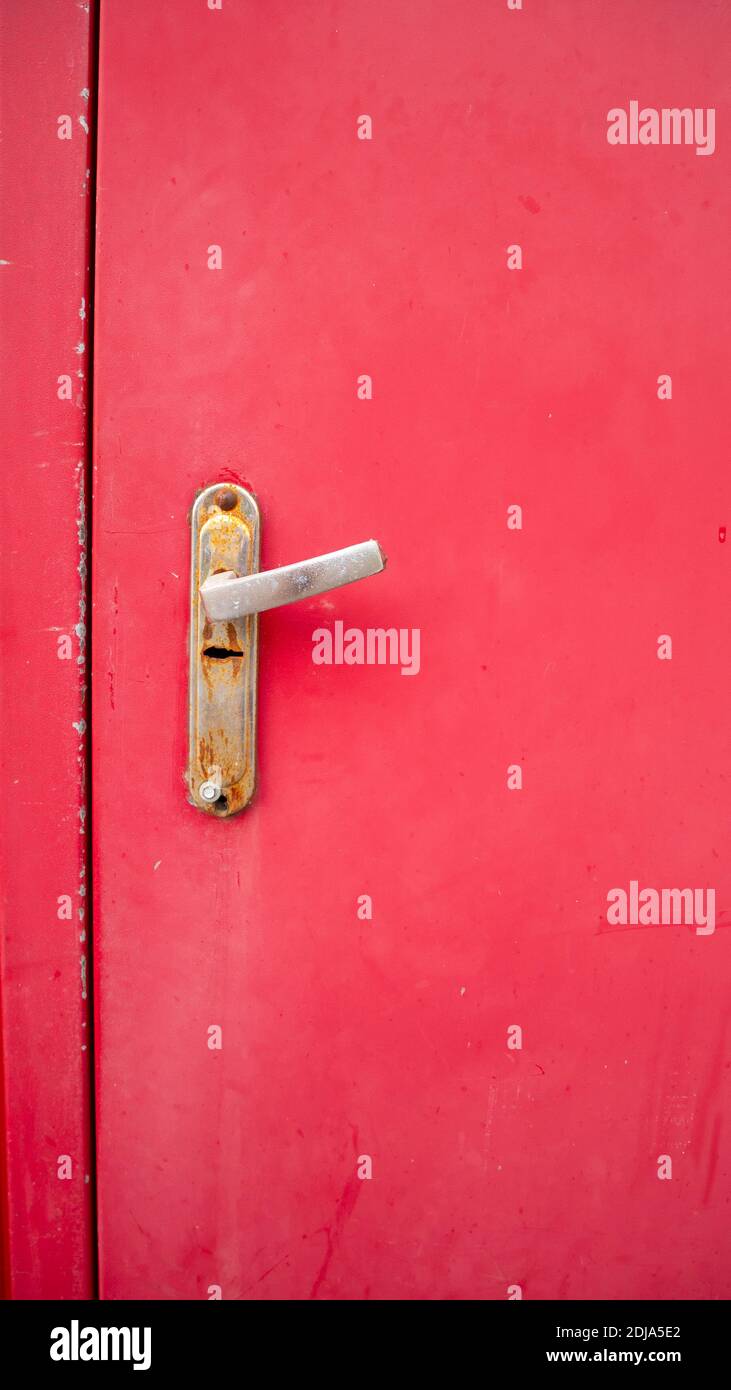 Red closed door with old handle. Rusty hardware with a lock. Worn paint ...