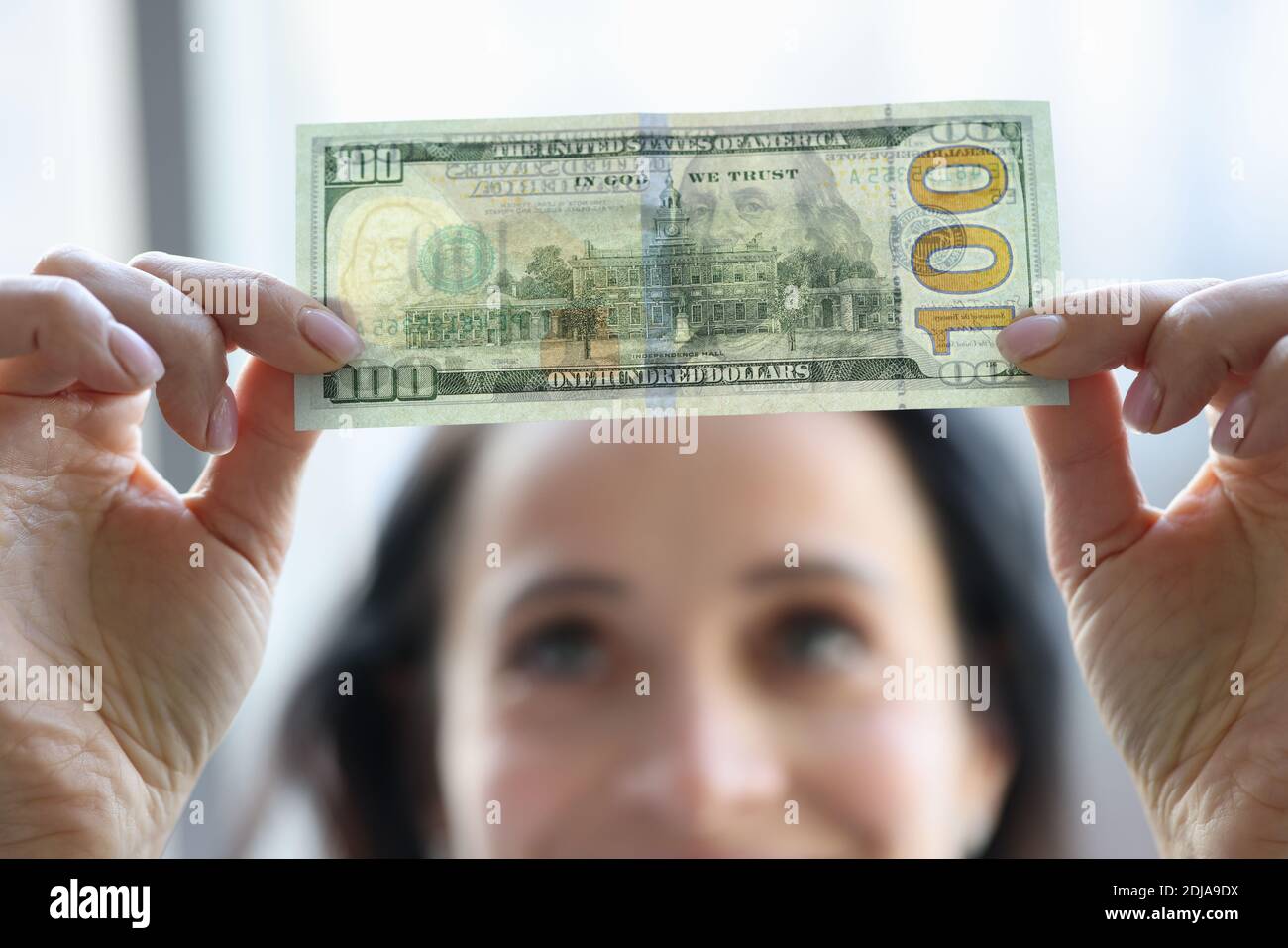 Woman holding dollar bill and looking at it with watermarks closeup ...