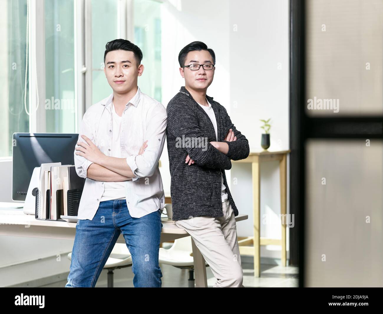 portrait of two young asian business men posing back to back in office ...