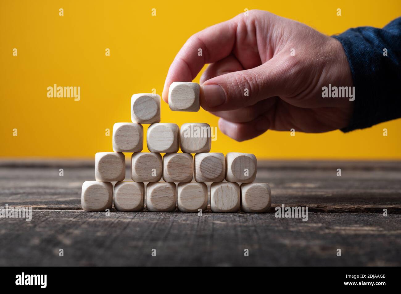 Male hand building a pyramid of wooden dices in a conceptual image ...