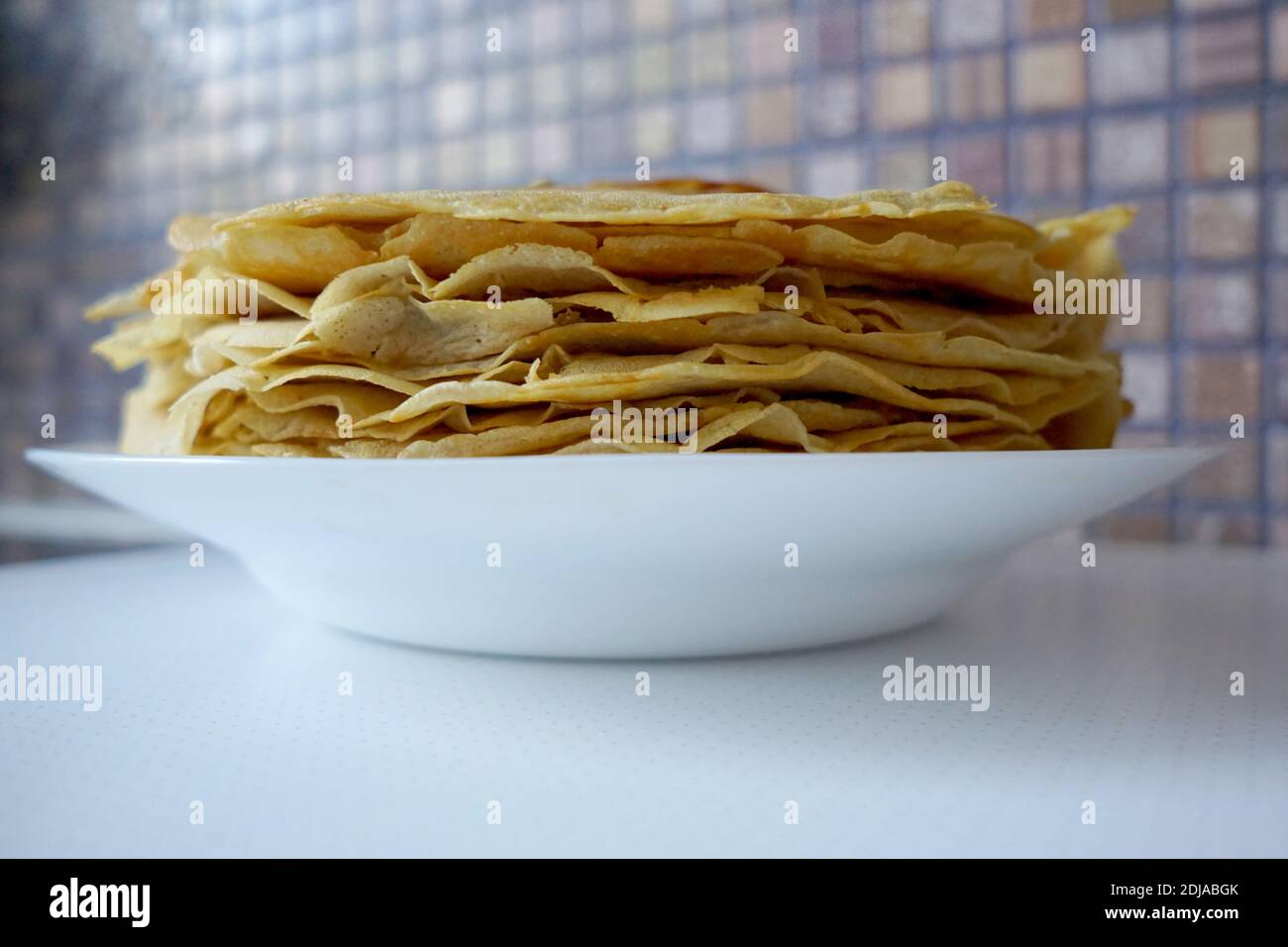 Thin crispy pancakes on a white plate and a light table on the ...