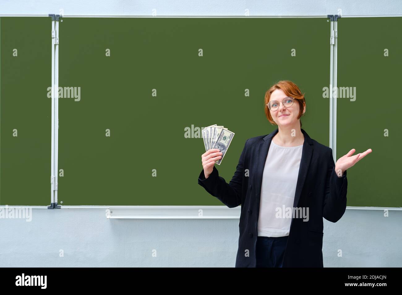 Happy teacher holding money, us dollars at the blackboard, copy space ...