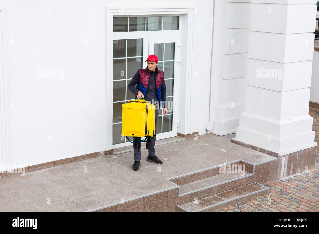 Portrait of a cheerful delivery man standing with yellow thermo ...